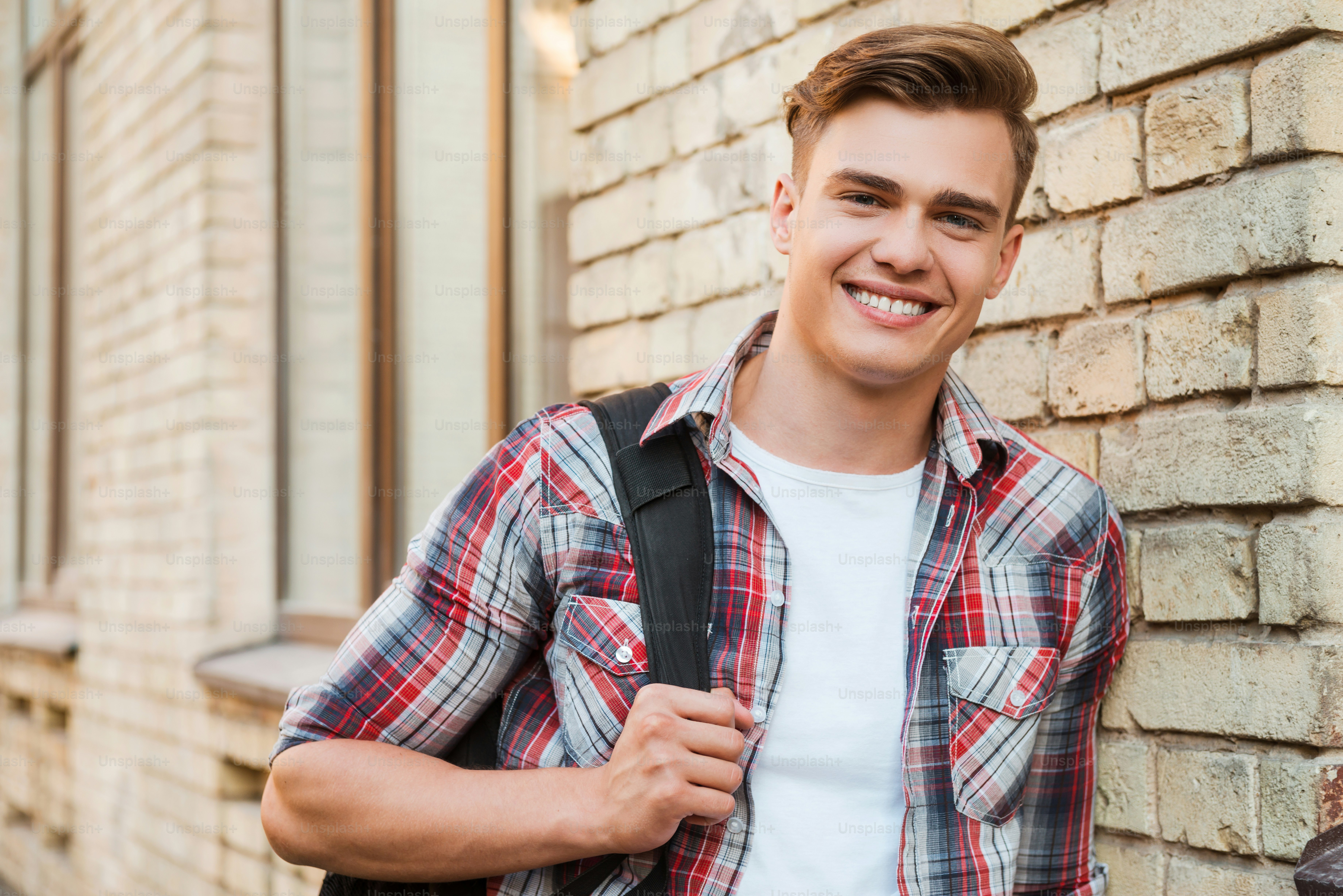 Handsome young man carrying backpack on one shoulder and smiling while ...