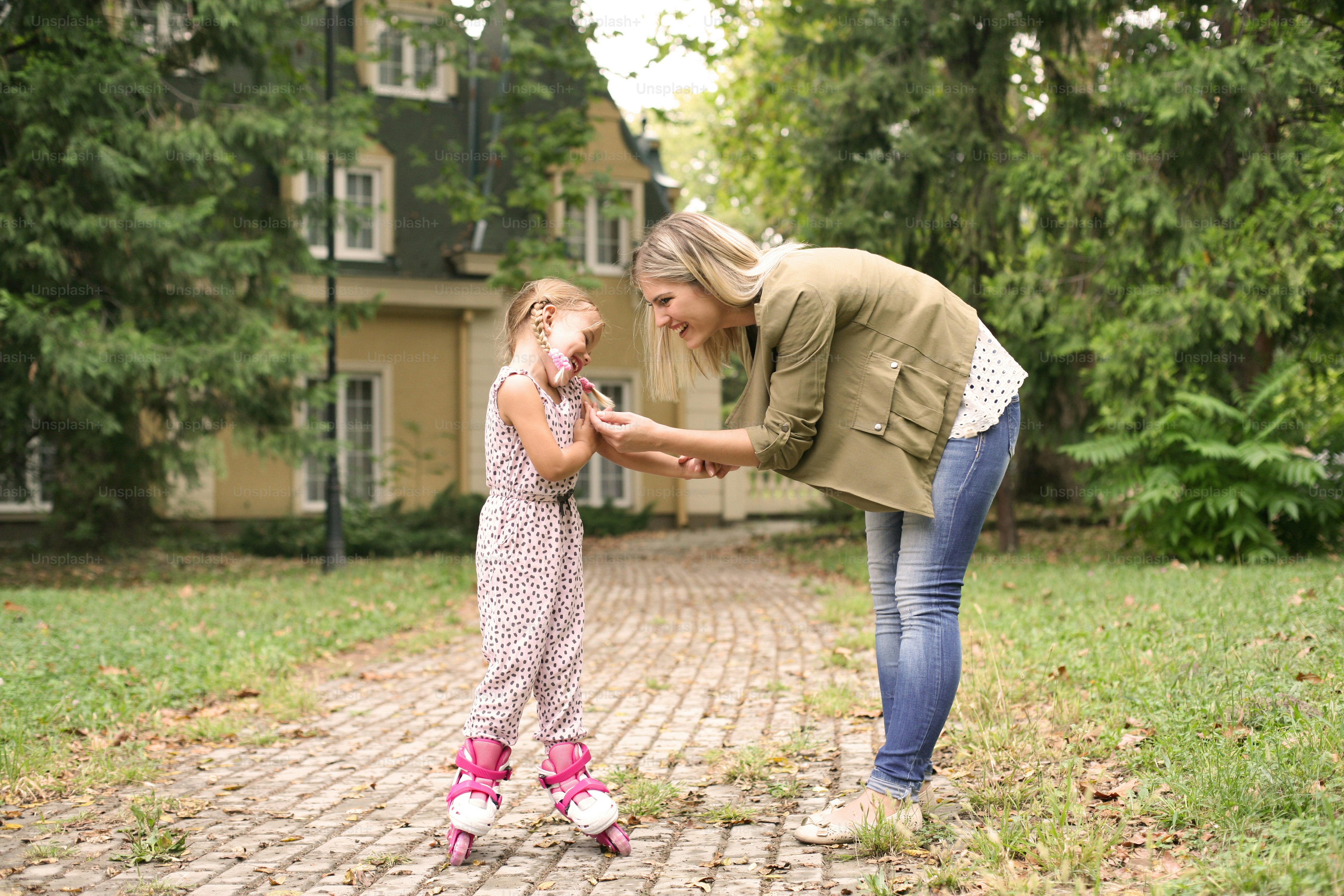 Cheerful mother assisting her little girl in rollerblading and having ...