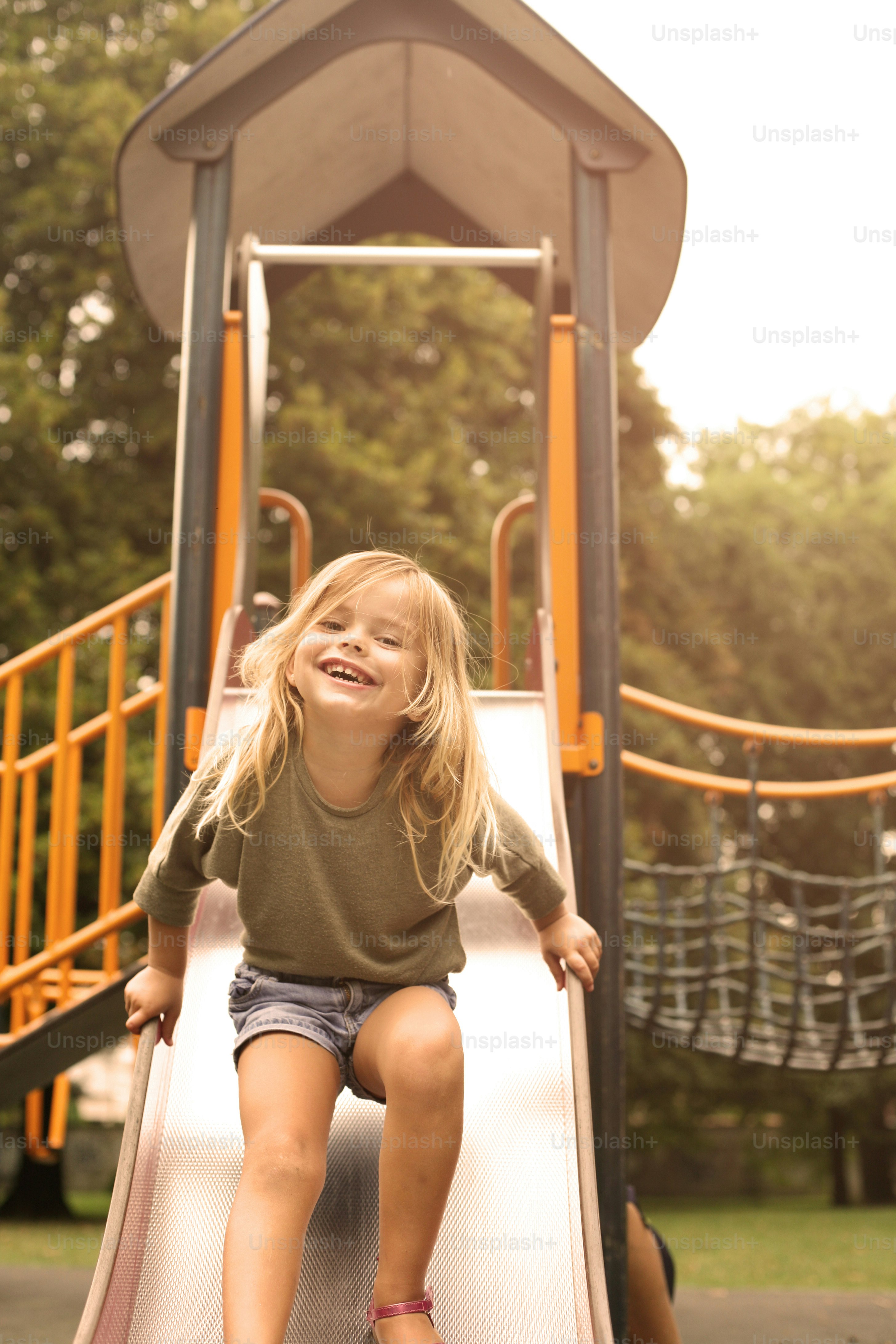 Little girl sliding down a slide in a playground. photo – Playground ...