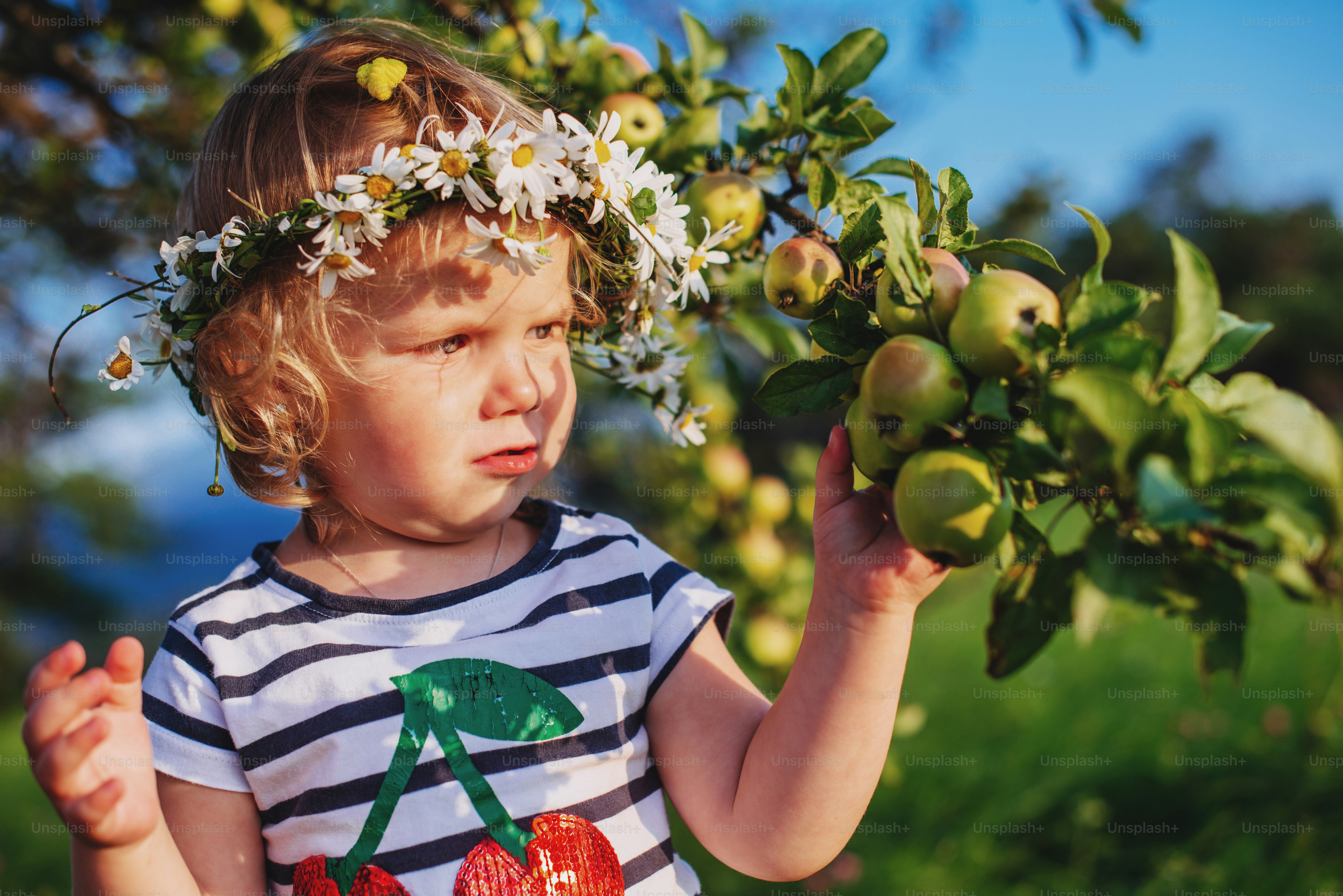 Little cute girl with a wreath on his head in the garden near the tree ...