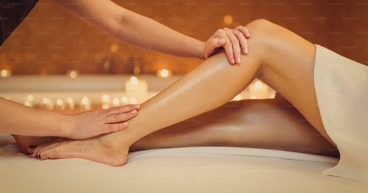 여성 다리의 마사지를받는 숙련 된 미용사 팔의 클로즈업 젊은 여자가 수건으로 덮인 마사지 테이블에 누워 있다 사진