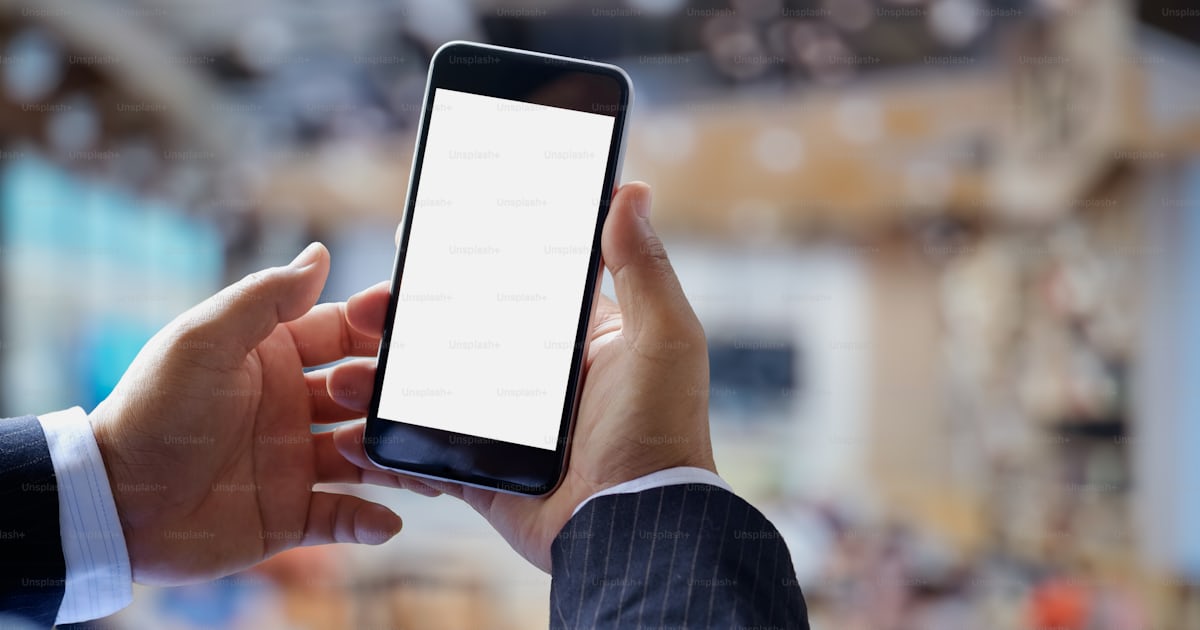カフェで休んでいるときにスマートフォンを使用し、空白の画面を見ているビジネスマンのトリミングされた画像。グラフィックディスプレイモンタージュ用