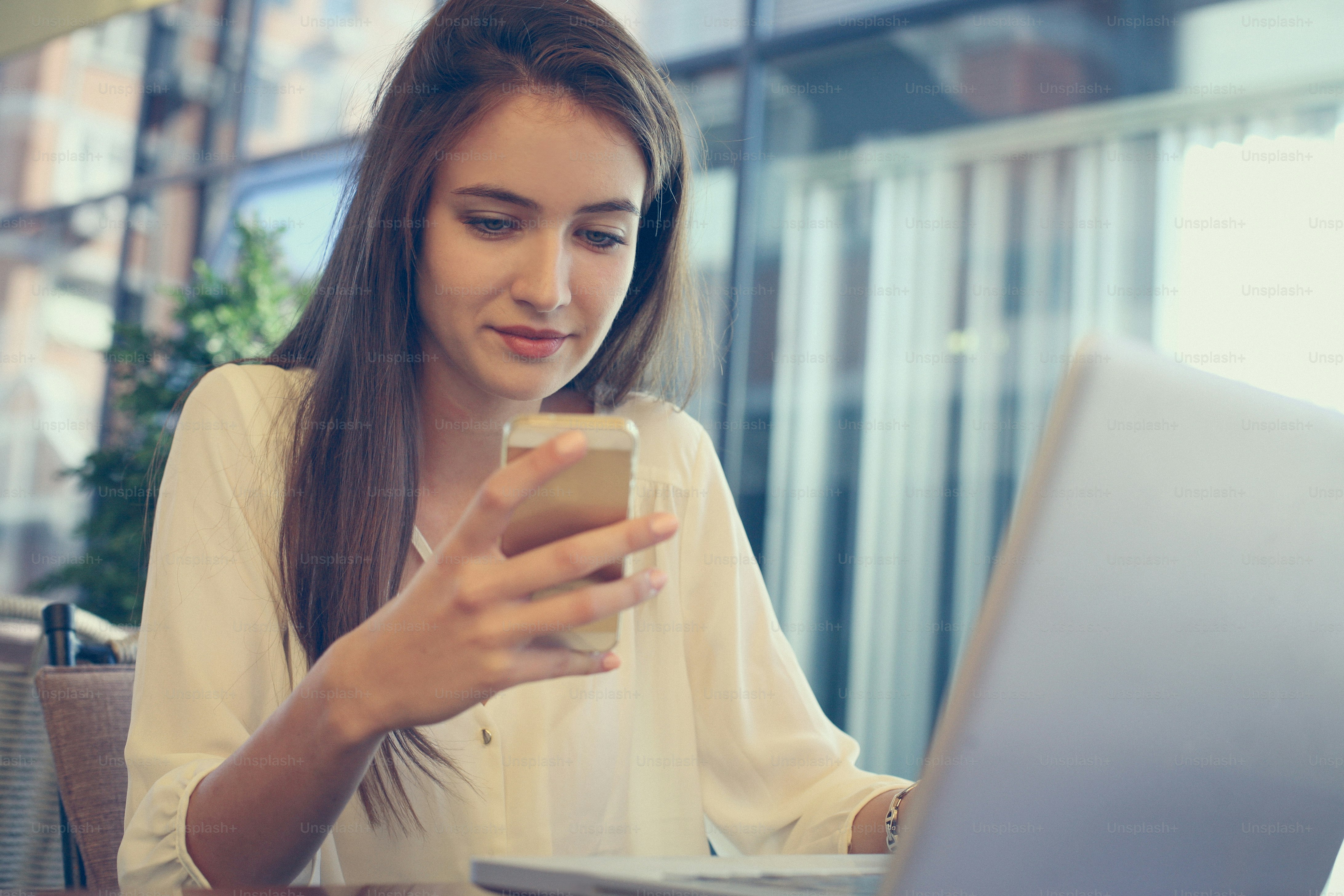 Businesswoman using laptop and texting with cell phone in office. photo ...