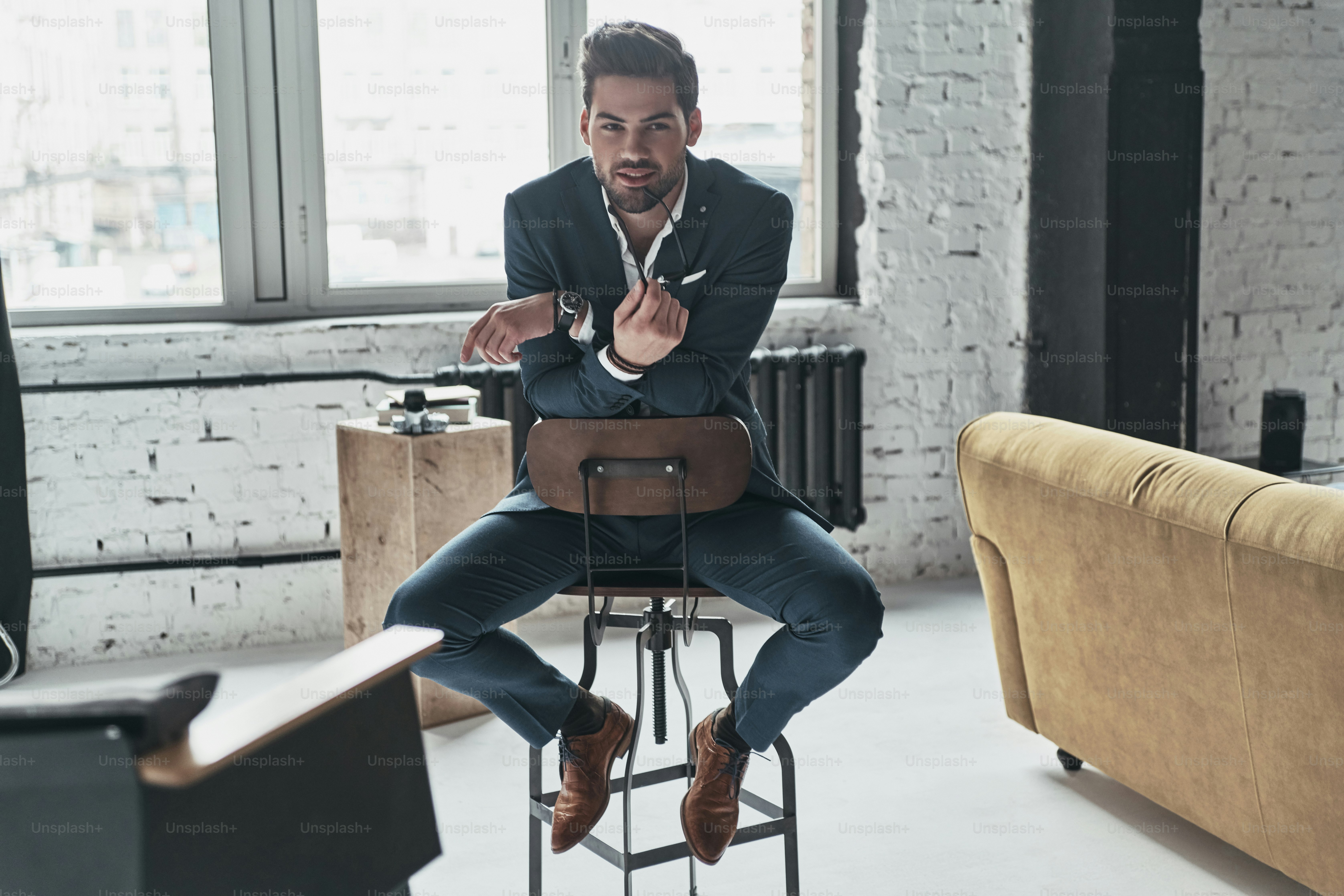 Close-up of young man in full suit sitting on the stool while spending ...
