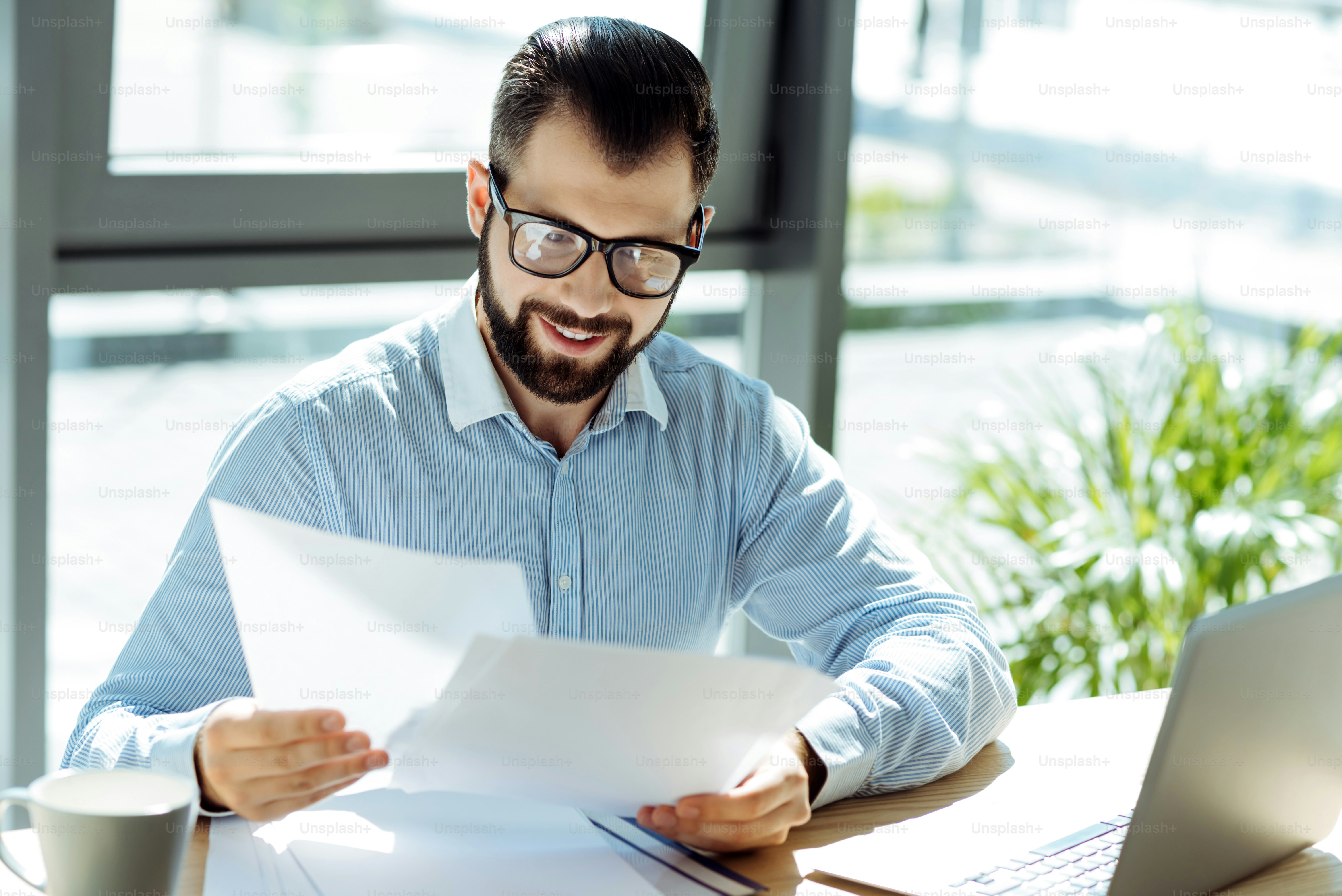 Careful inspection. Upbeat pleasant bearded man in glasses sitting in ...