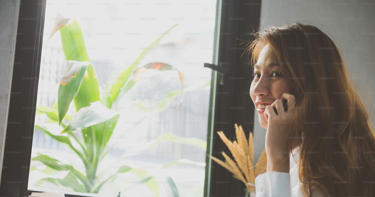 하얀 드레스를 입은 젊은 사업가가 카페의 테이블에 앉아 노트북에 글을 쓰고 있다 스마트폰과 커피 한 잔을 말하는 아시아 여성