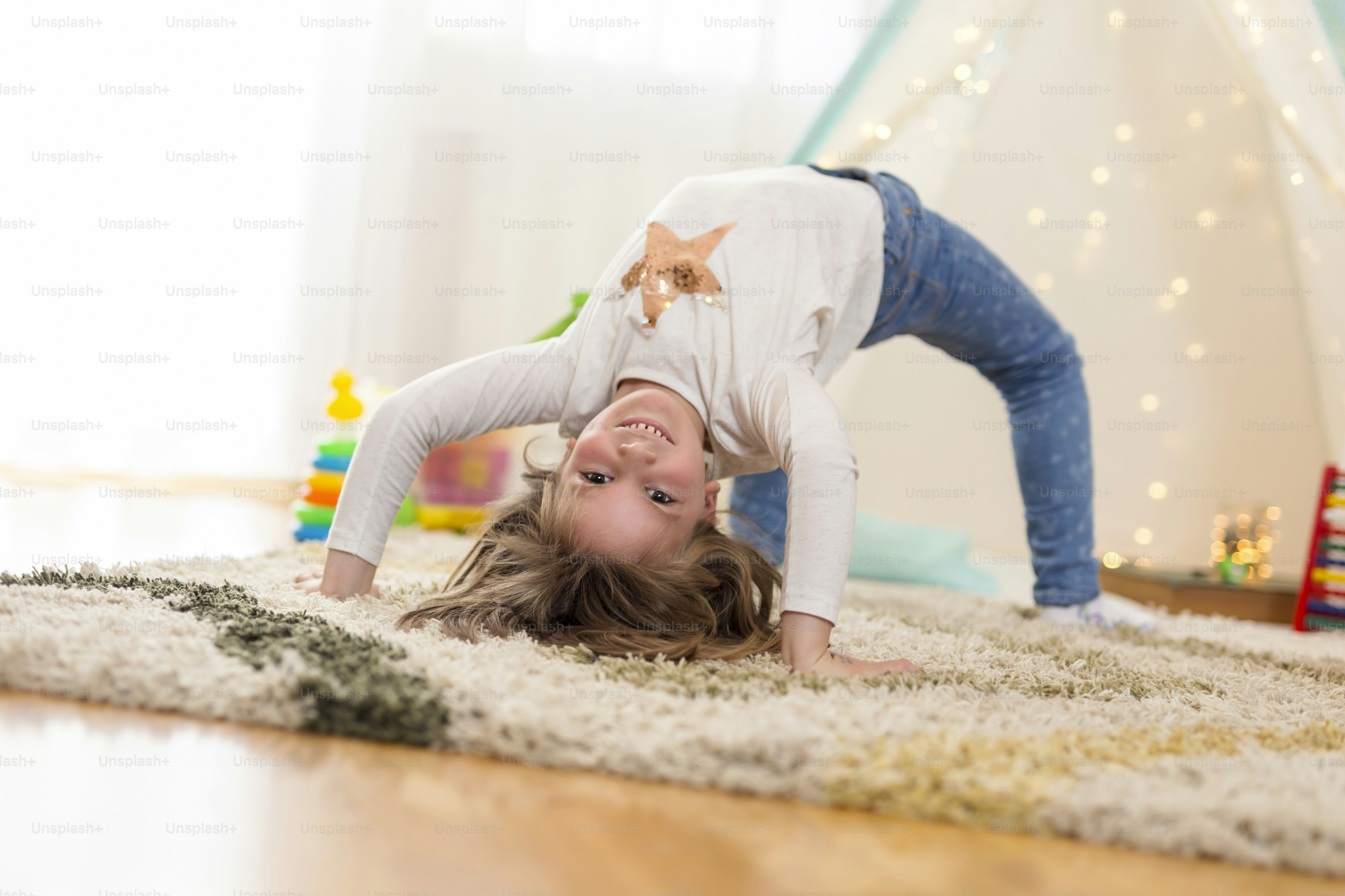 Cheerful little girl doing backbend, playing in her playroom and having ...