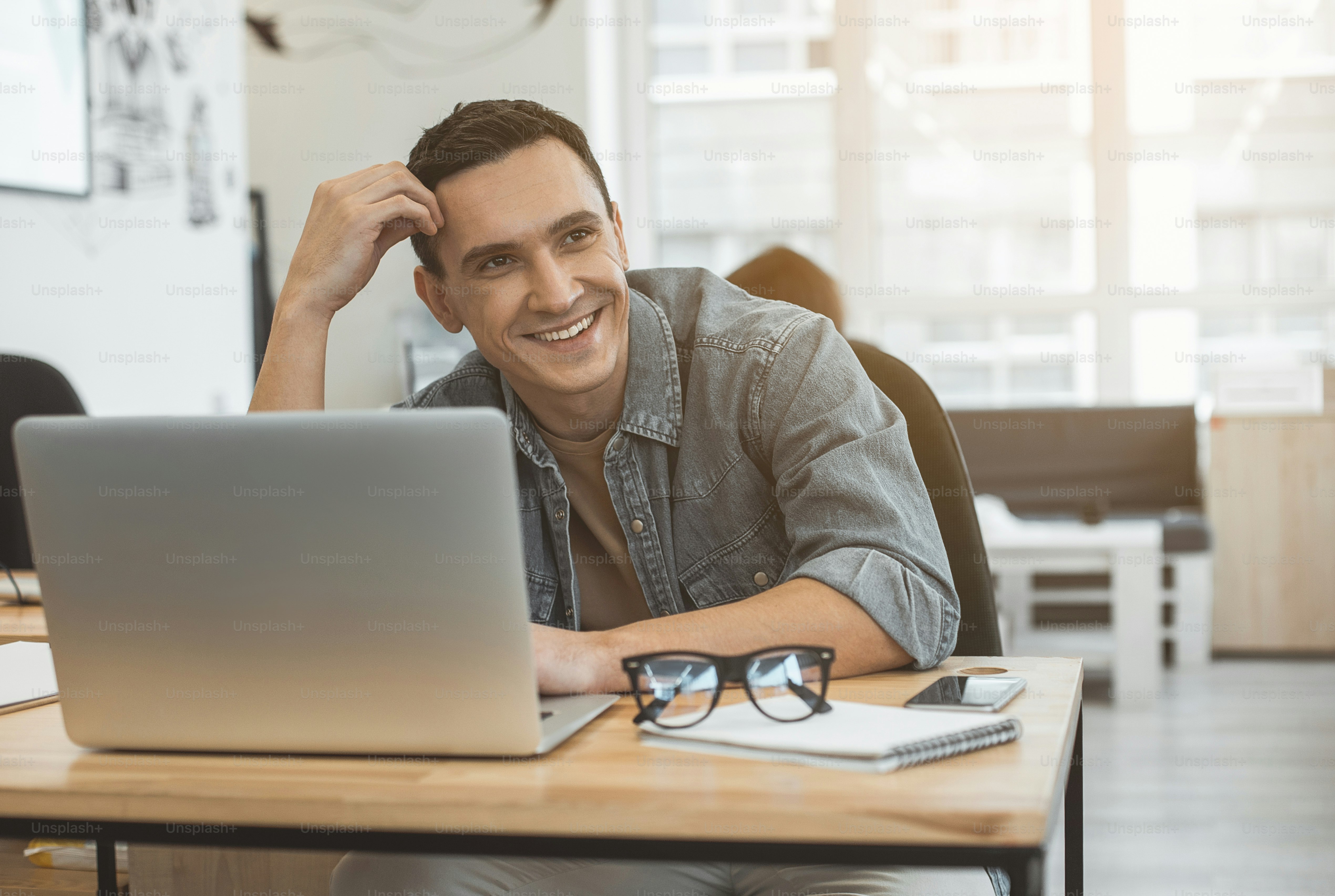 Portrait of cheerful man typing in laptop while sitting at desk in office. Beaming employee at ...