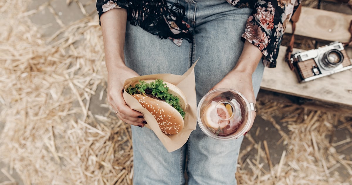 맛있는 햄버거와 레모네이드 상위 뷰 육즙이 많은 햄버거를 들고 상쾌한 칵테일을 들고 있는 세련된 힙스터 여성 길거리 음식