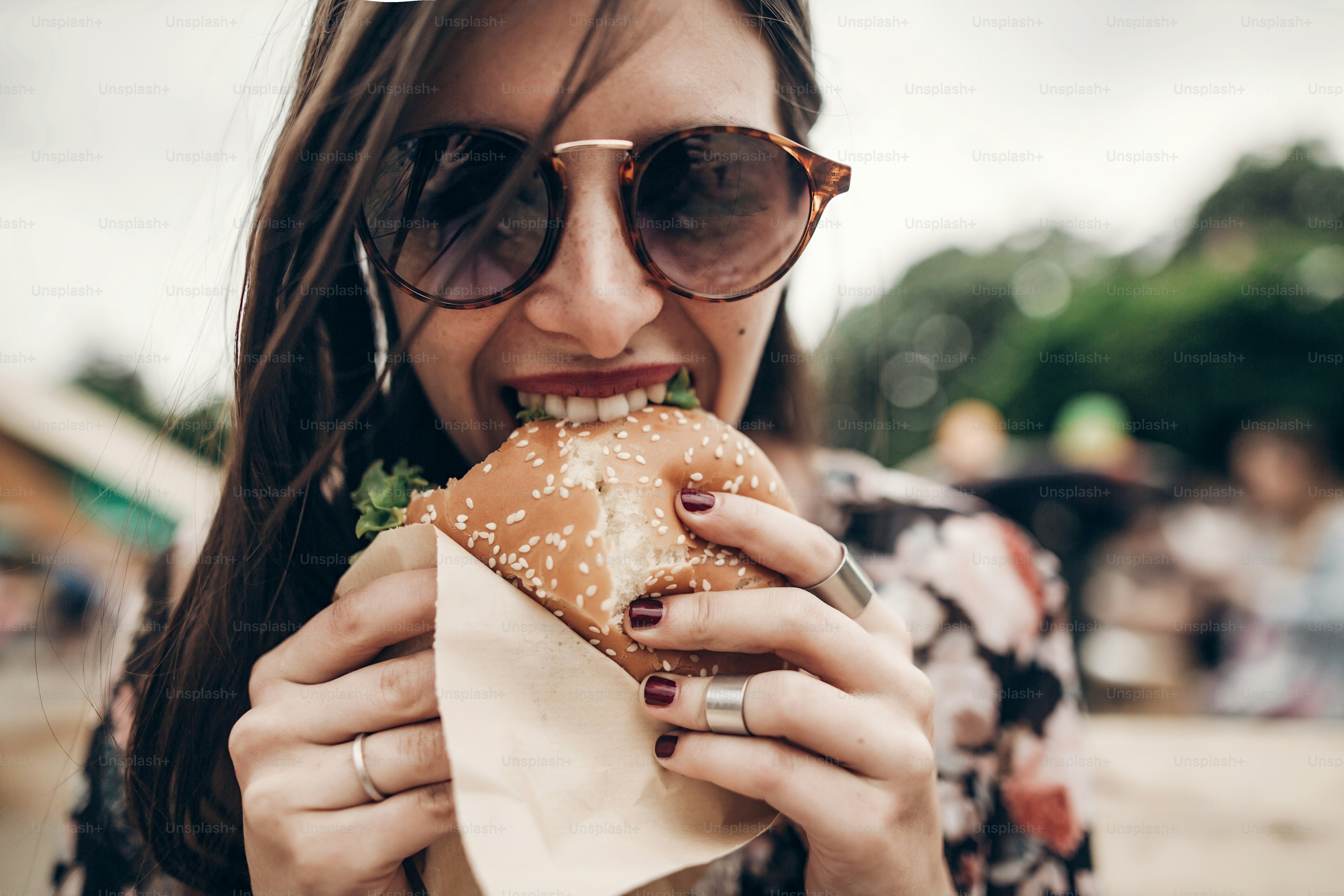 Stylish hipster woman holding juicy burger and eating. boho girl biting ...