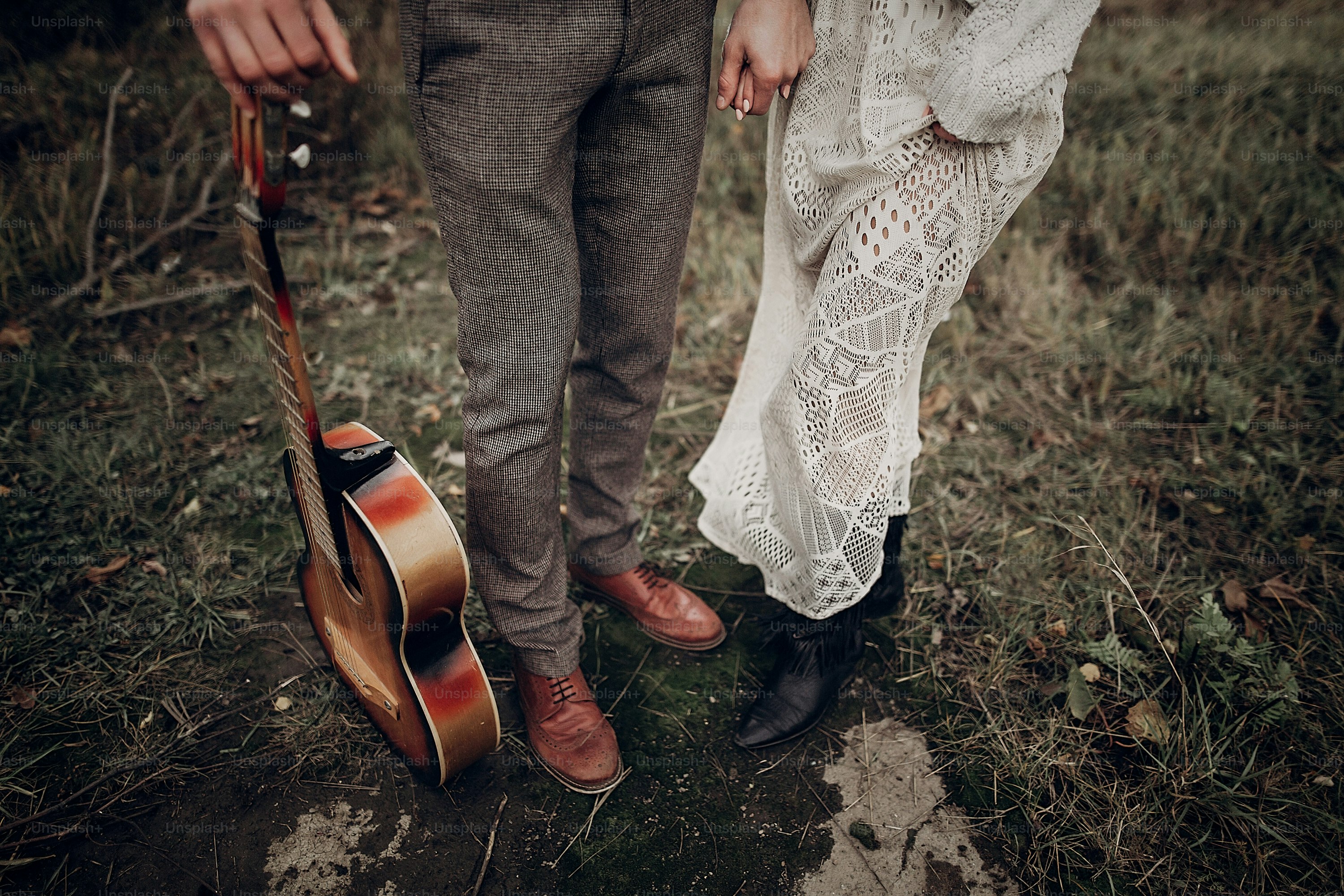 Homme avec guitare tenant la main avec sa femme gitane bohème gros plan dans un champ venteux ...