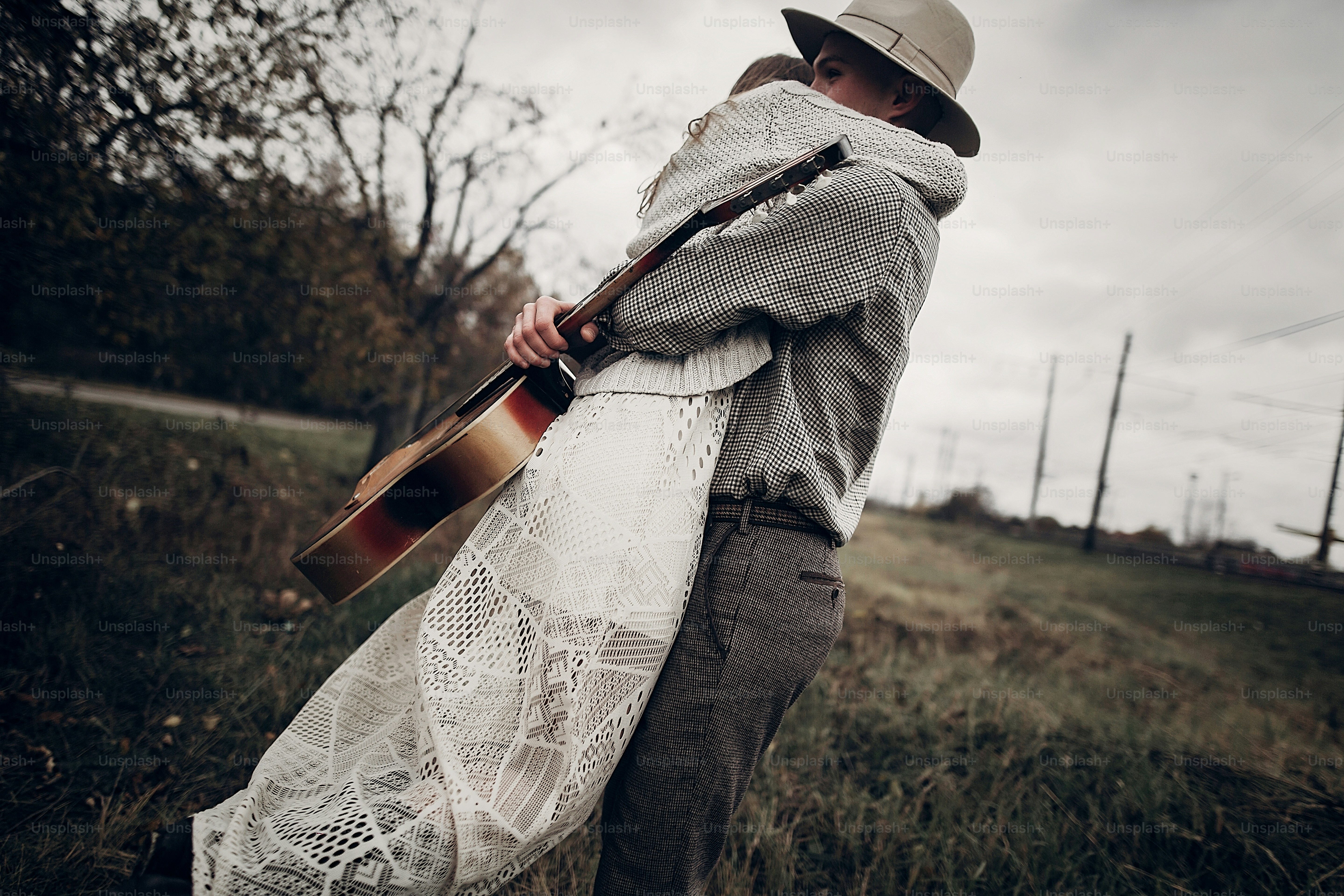 Stylish hipster couple hug in field, handsome cowboy musician with ...