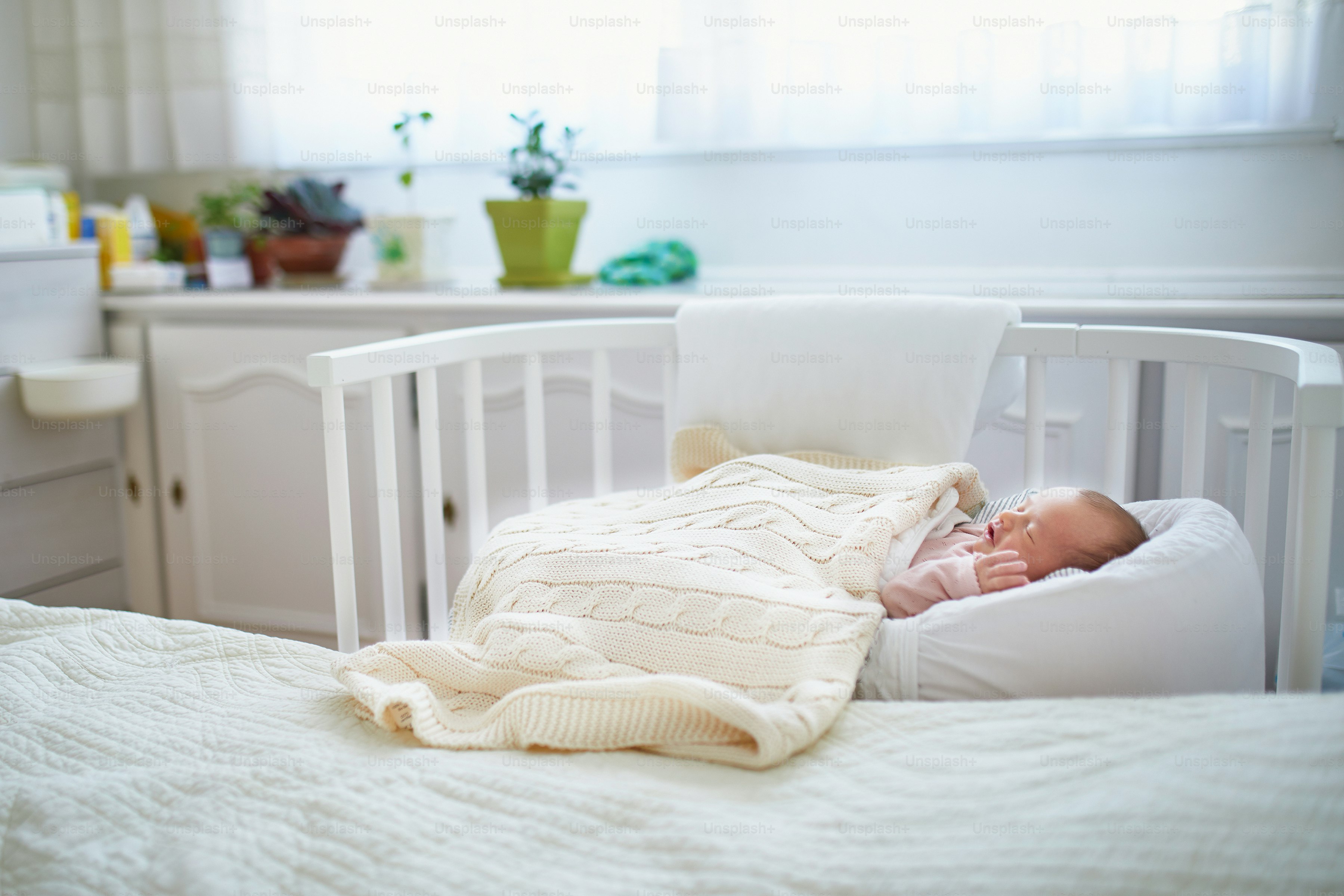 Newborn baby girl having a nap in co-sleeper crib attached to parents ...