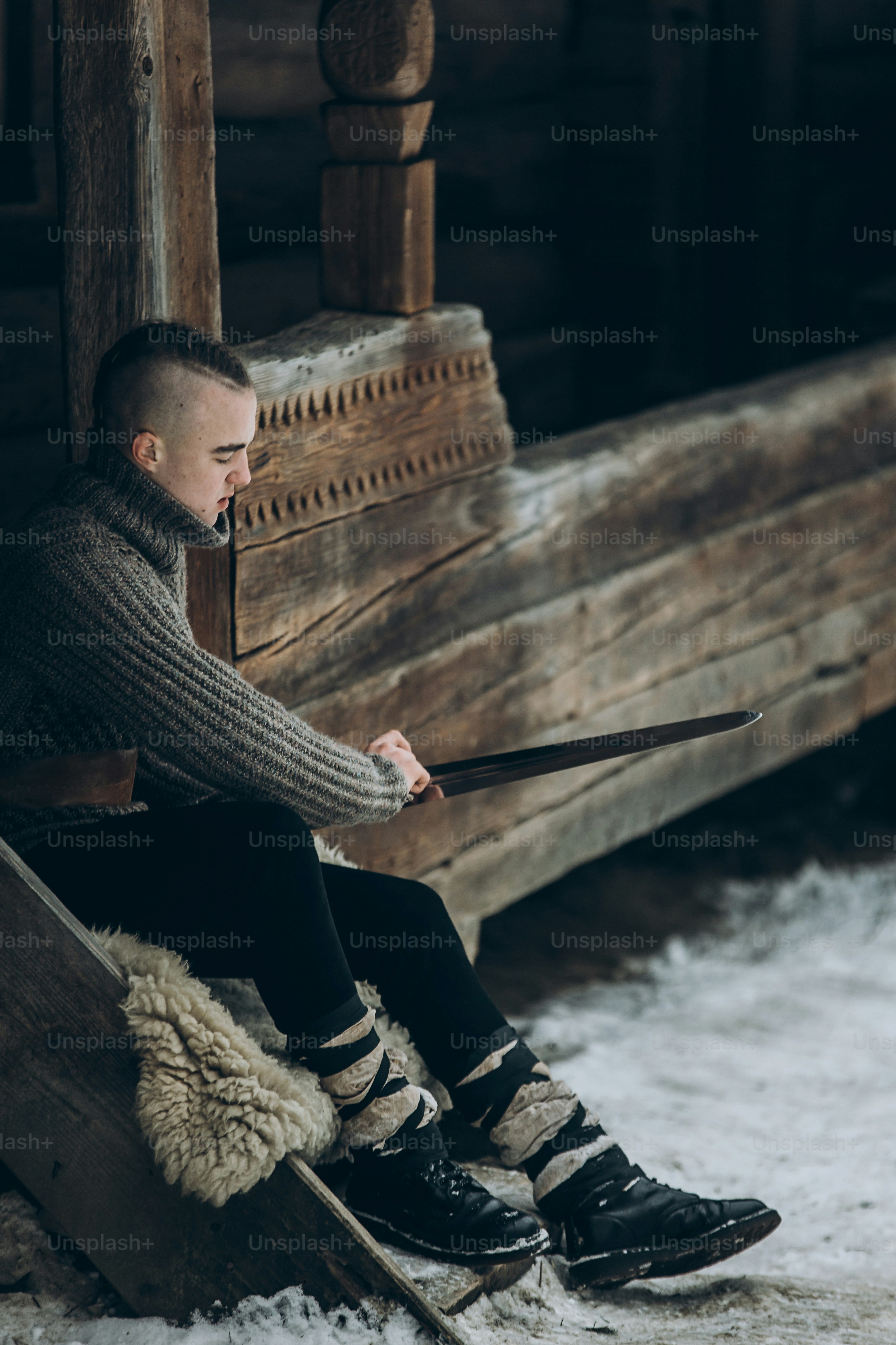 Strong viking warrior sharpening his sword while sitting near ancient ...