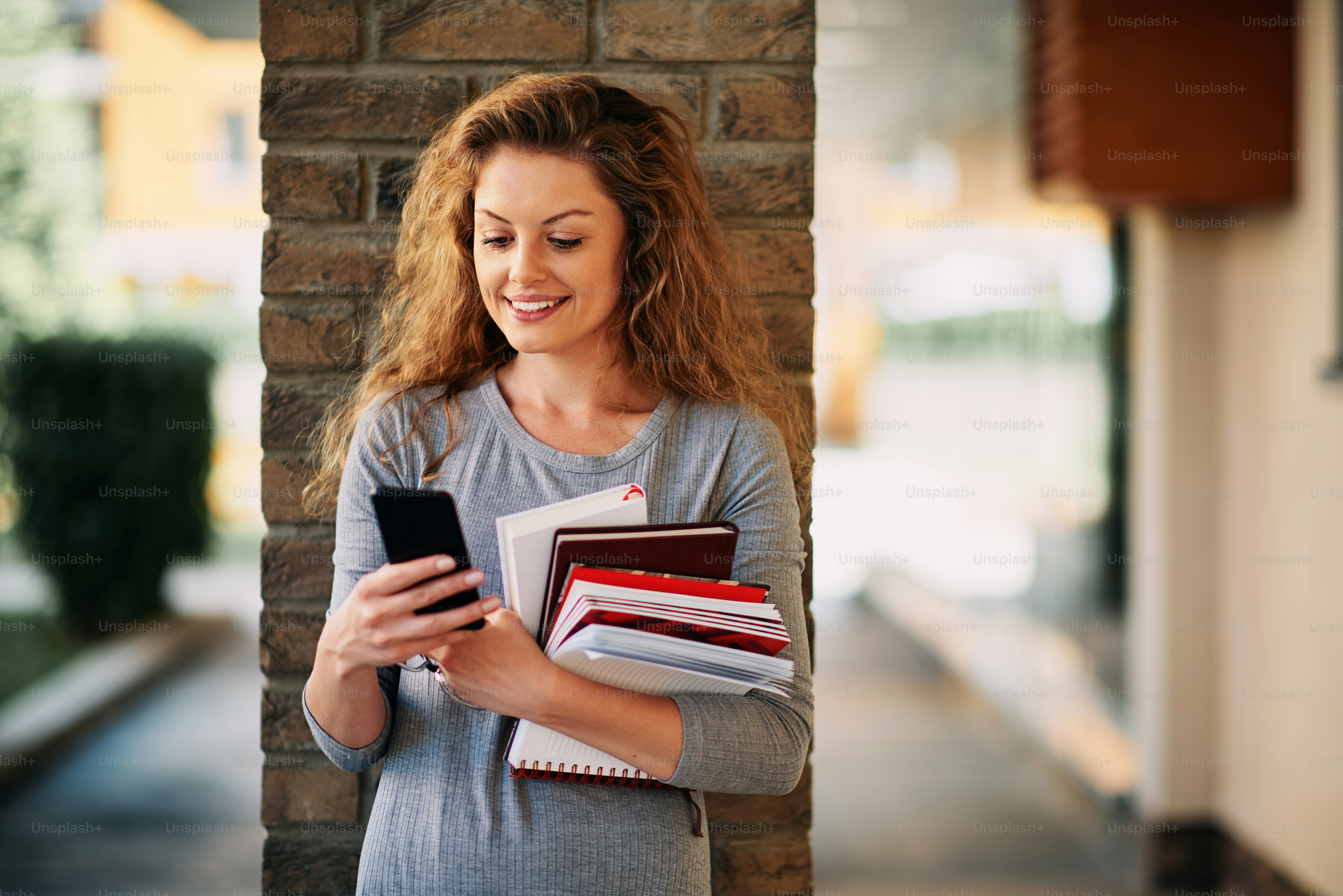 Female student using smartphone and holding books. photo – Portrait ...