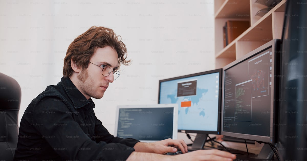 ソフトウェア開発会社のオフィスで多くのモニターを備えたデスクトップコンピューターで作業している男性プログラマー。webサイトのデザイン