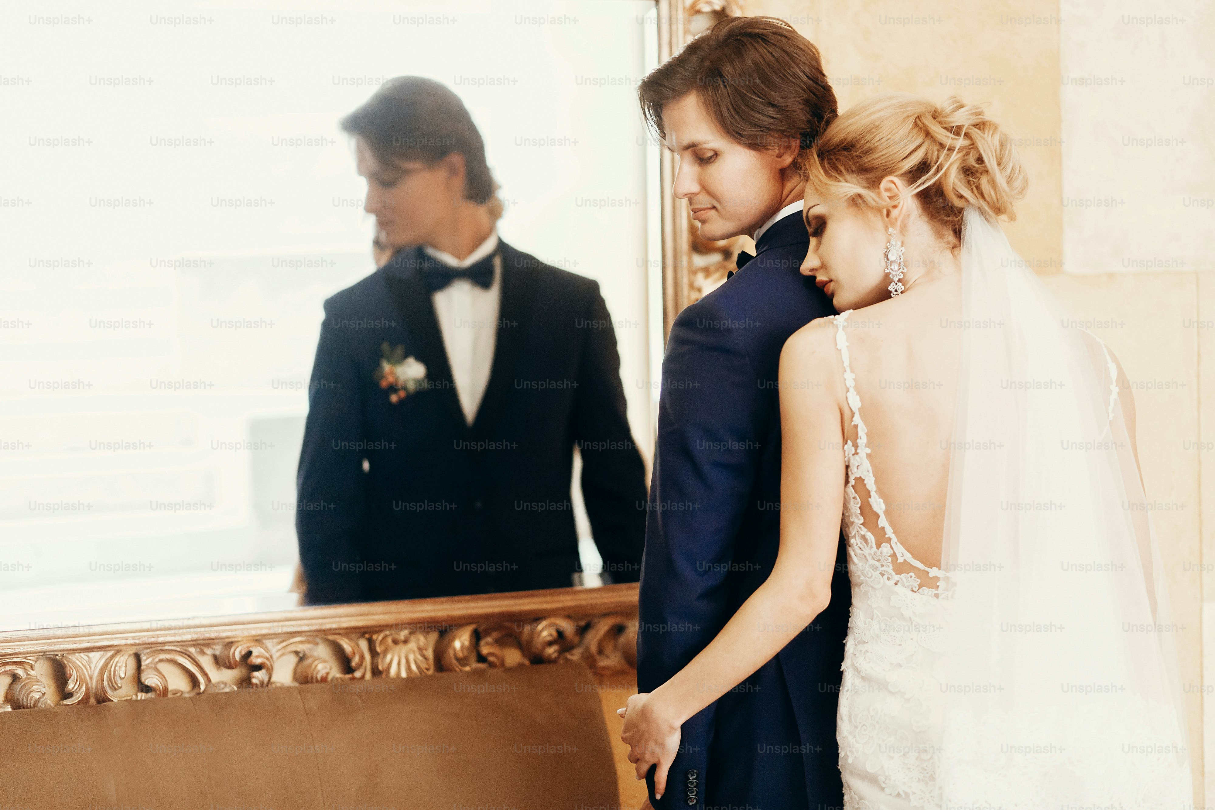 Stylish bride and groom posing at big mirror in hotel room. happy ...