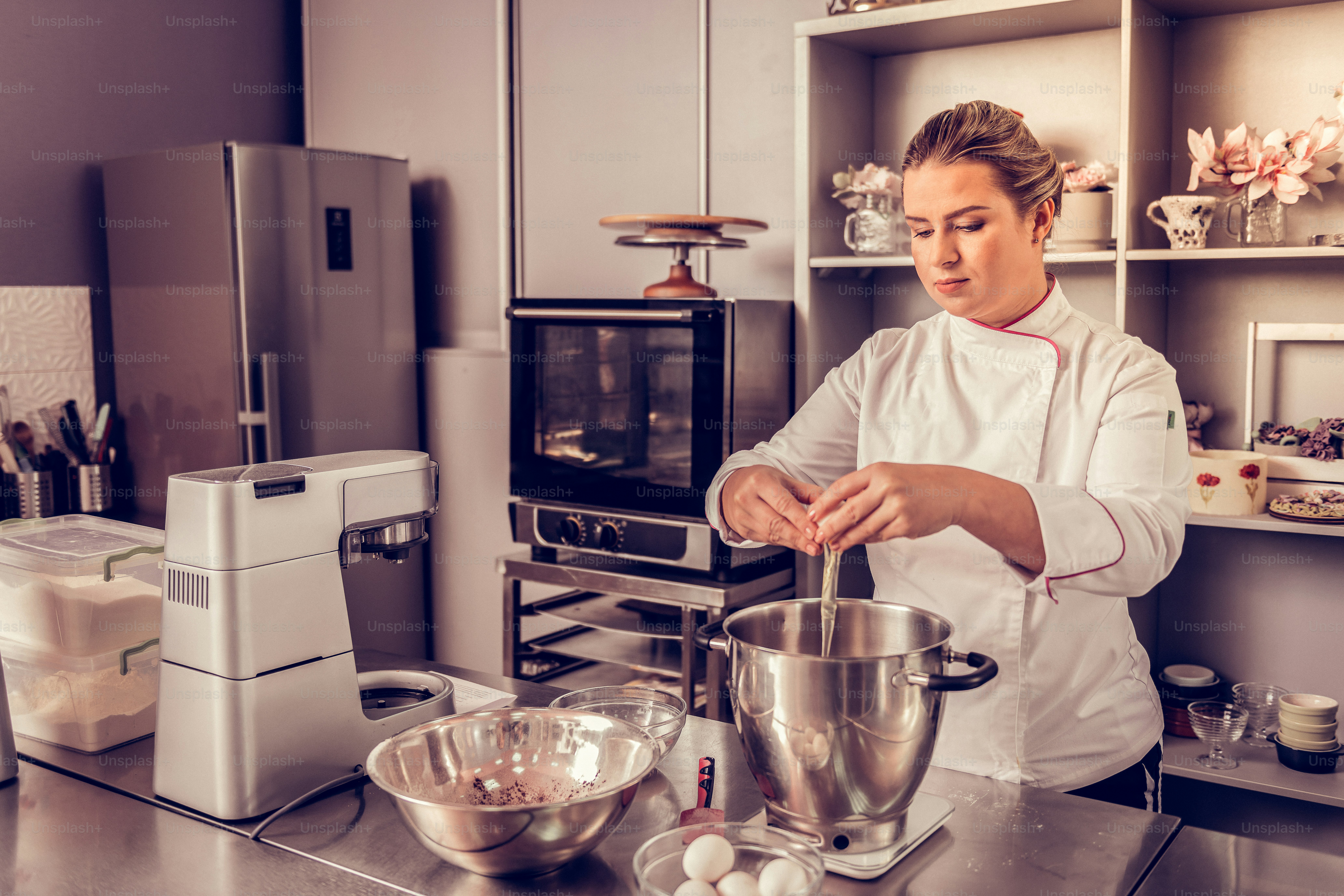 Sponge cake preparation. Nice pastry chef adding eggs to the bowl while ...