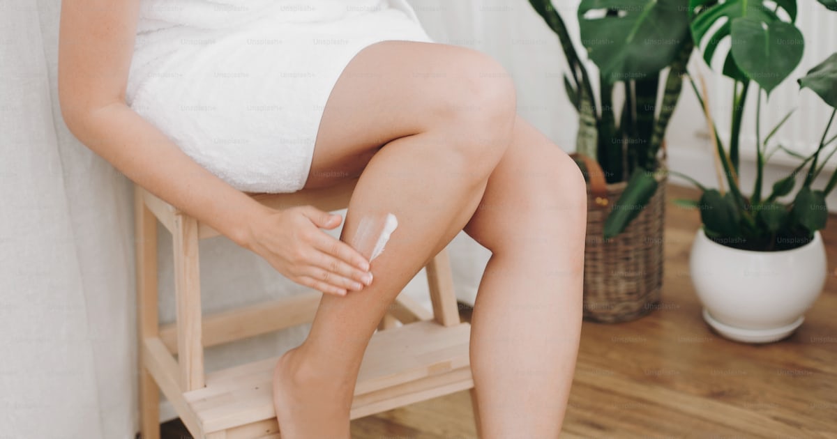 녹색 식물로 욕실에서 면도한 후 다리에 크림을 바르는 젊은 여성 피부 관리 및 웰빙 개념 부드러운 피부 결과를 위해 다리를