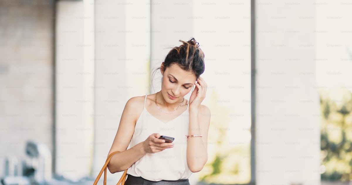 세련된 웃는 여자는 걷고 쓰거나 스마트 폰에서 온라인으로 Sms 메시지를 읽으며 화면을보고 바람은 거리 오래된 공항 기차역