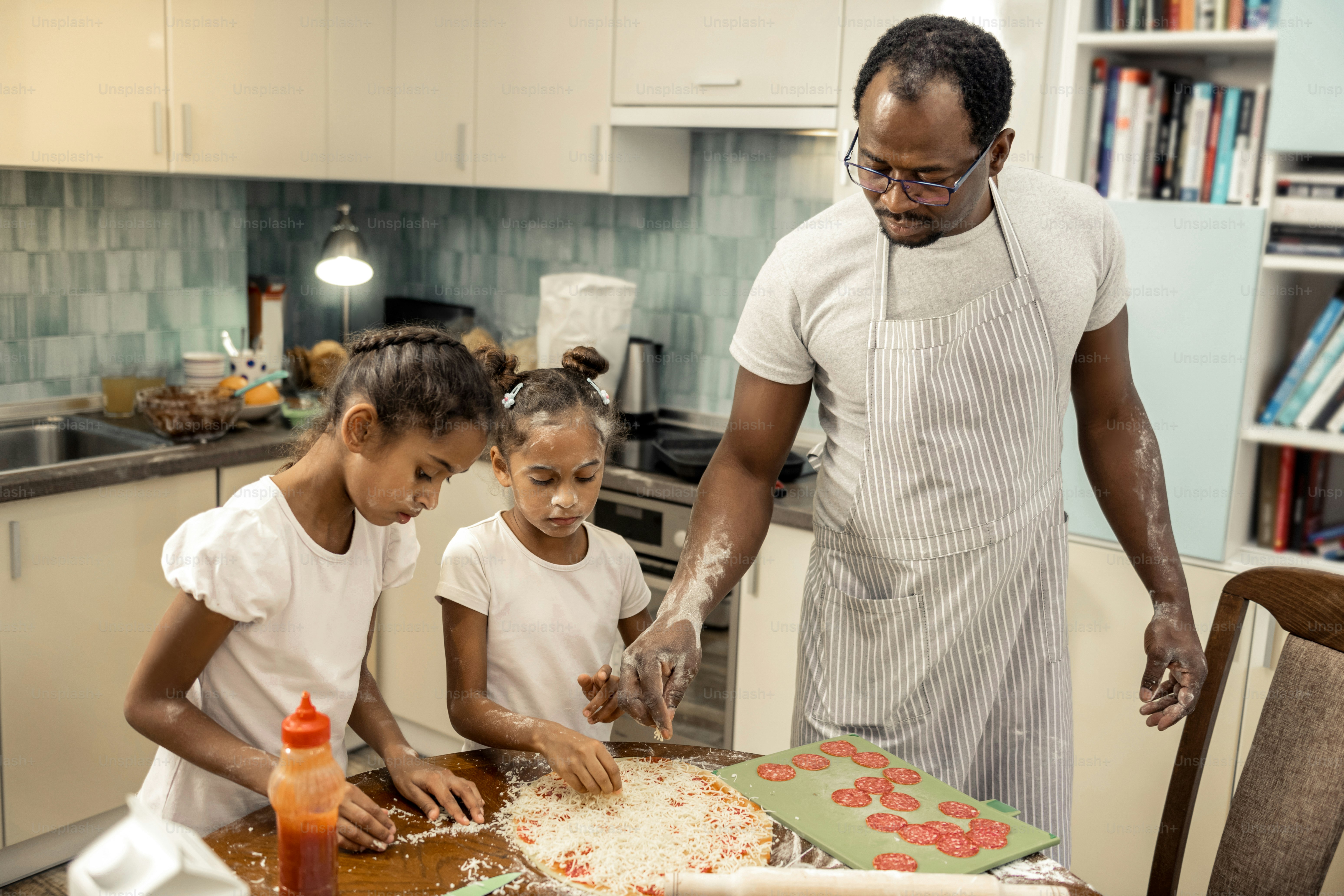 Helpful father. Father wearing striped apron helping his little girls ...