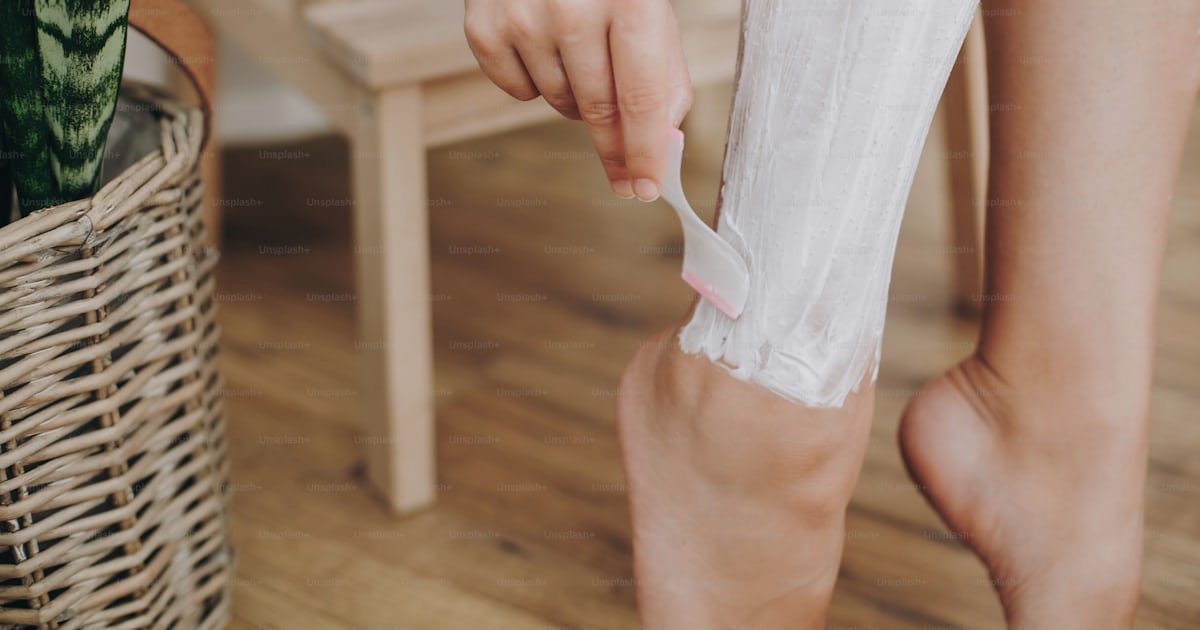 제모 개념 탈모 과정 흰 수건을 쓴 젊은 여성이 다리에 면도 크림을 바르고 녹색 식물이 있는 집 욕실에서 플라스틱 면도기를