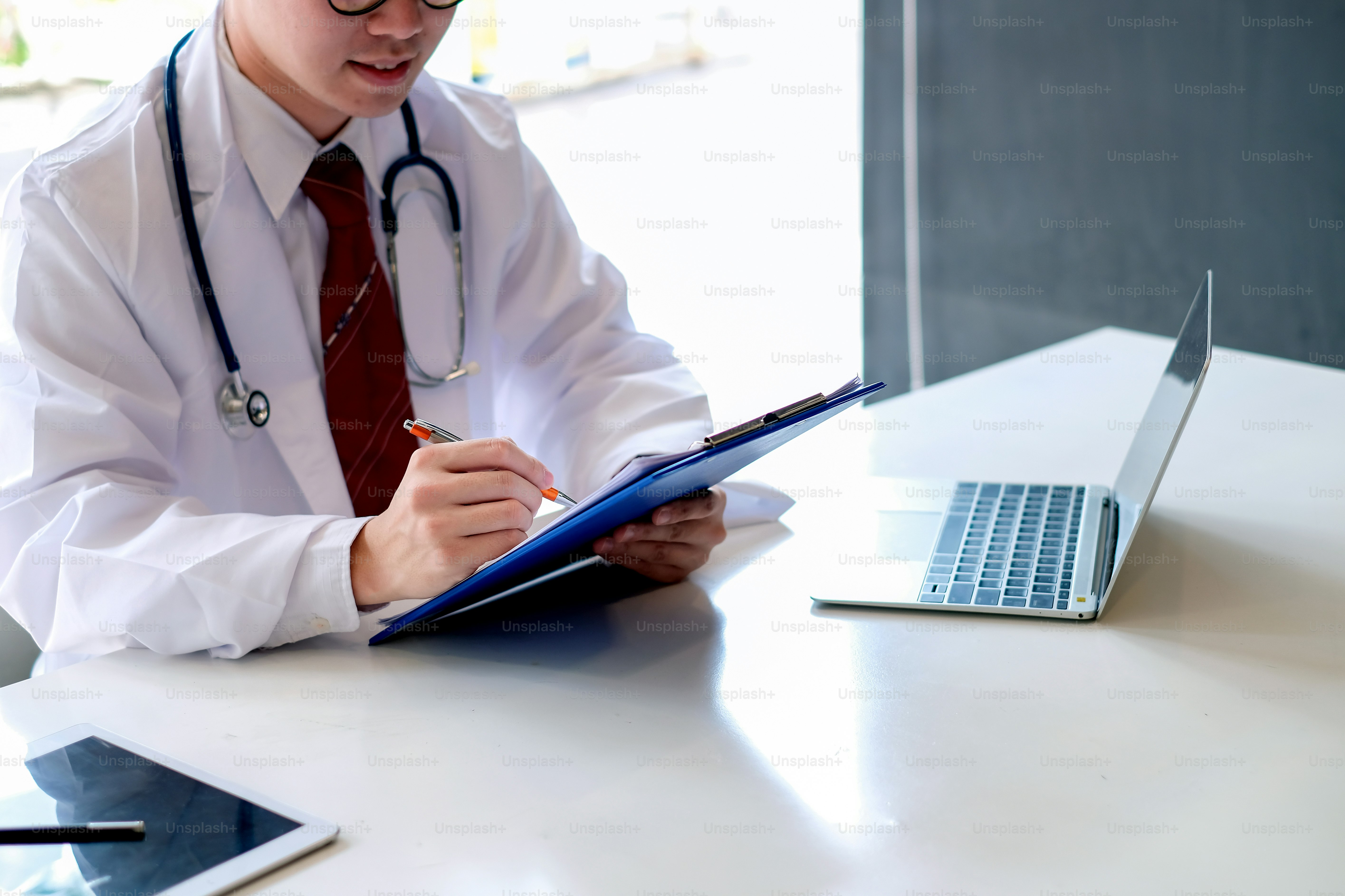 Doctor working on his laptop with taking note patient information at ...