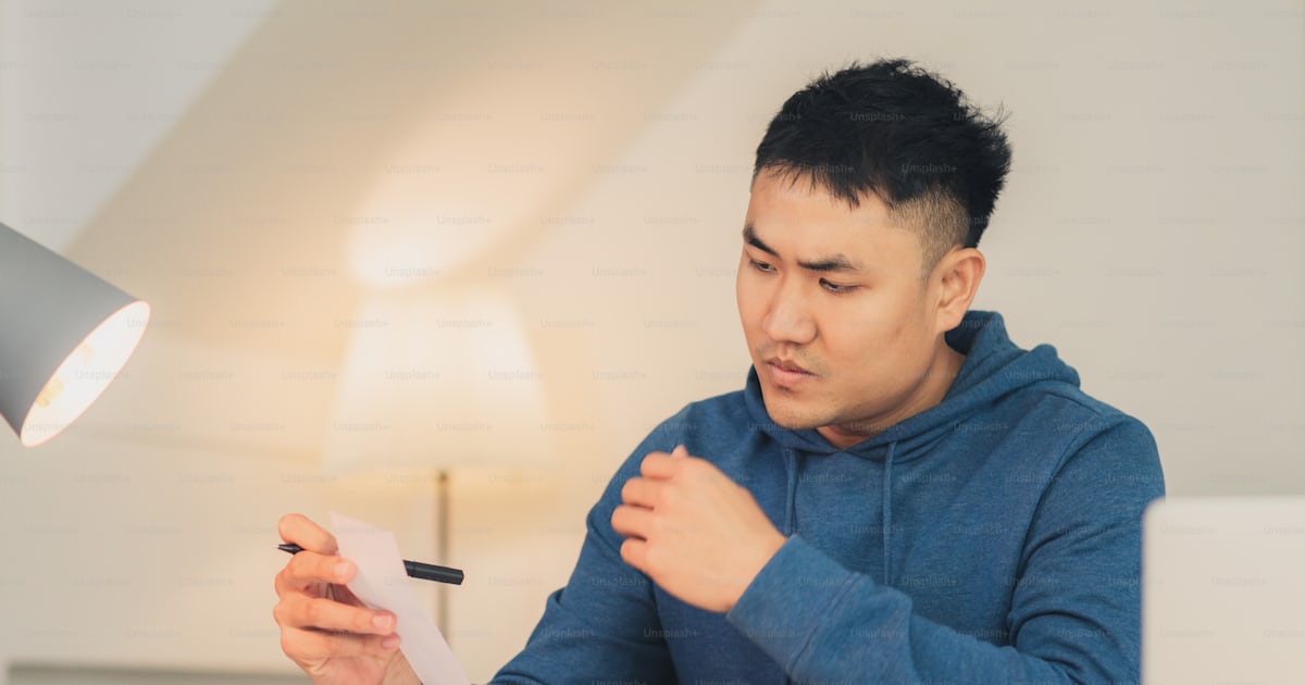 아름 다운 젊은 웃는 아시아 남자는 집에서 거실에서 책상에서 노트북을 작업 하 고 있습니다 홈 오피스에서 노트북 문서 금융 및