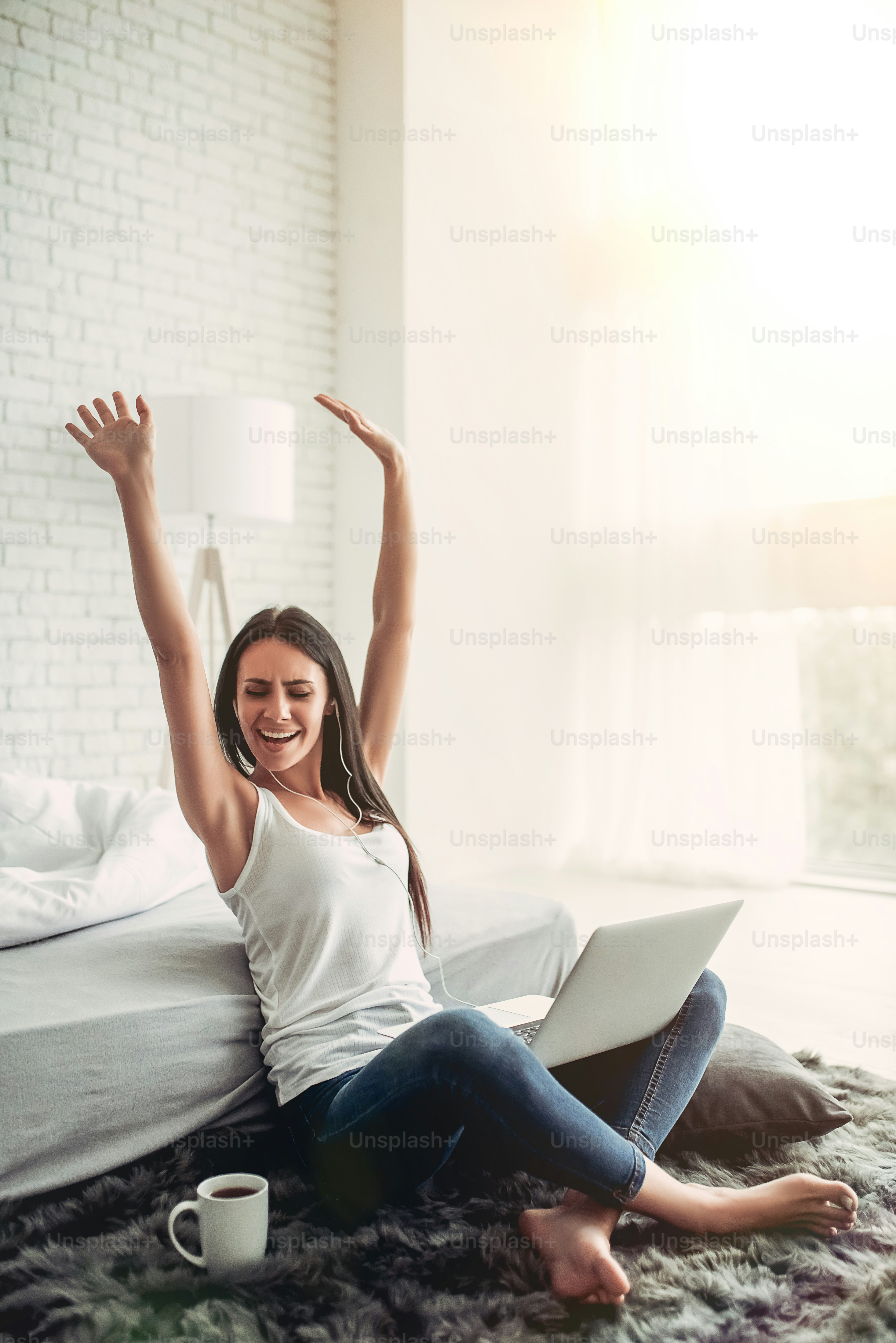 Happy young woman in earphones is listening to music and singing while ...