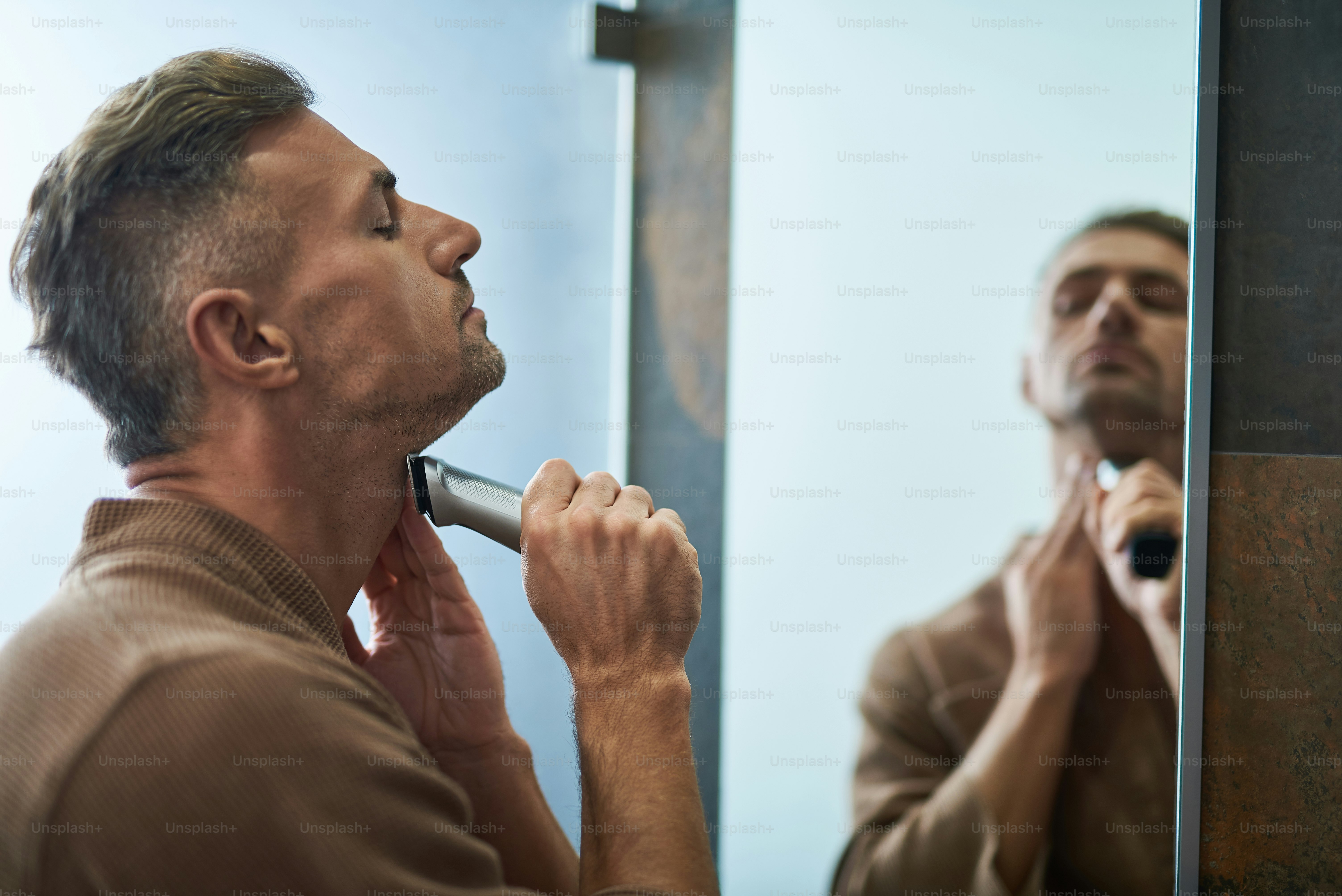 Side view portrait of handsome young gentleman using electric shaving ...