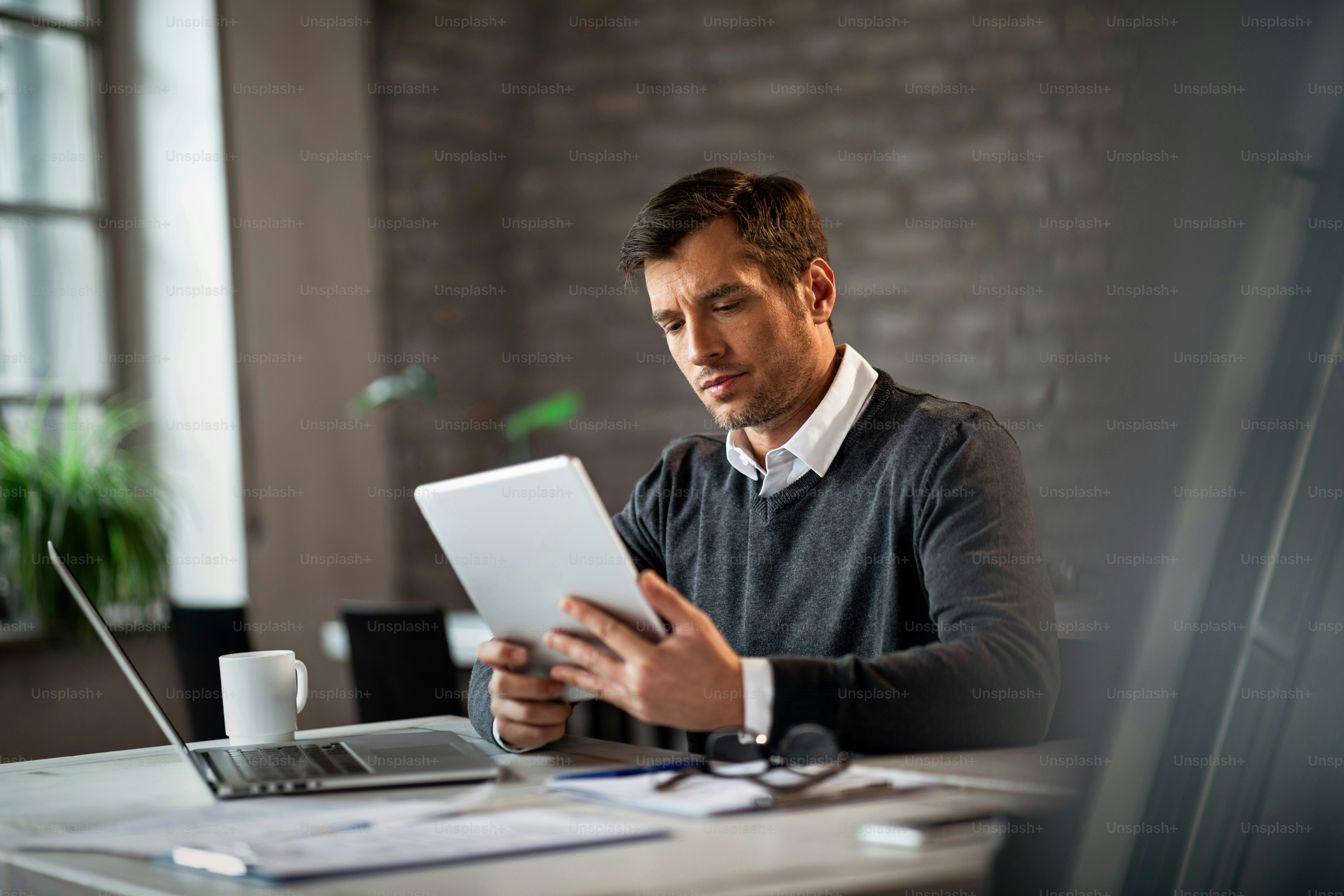 Freelance worker surfing the net on digital tablet while working at his ...