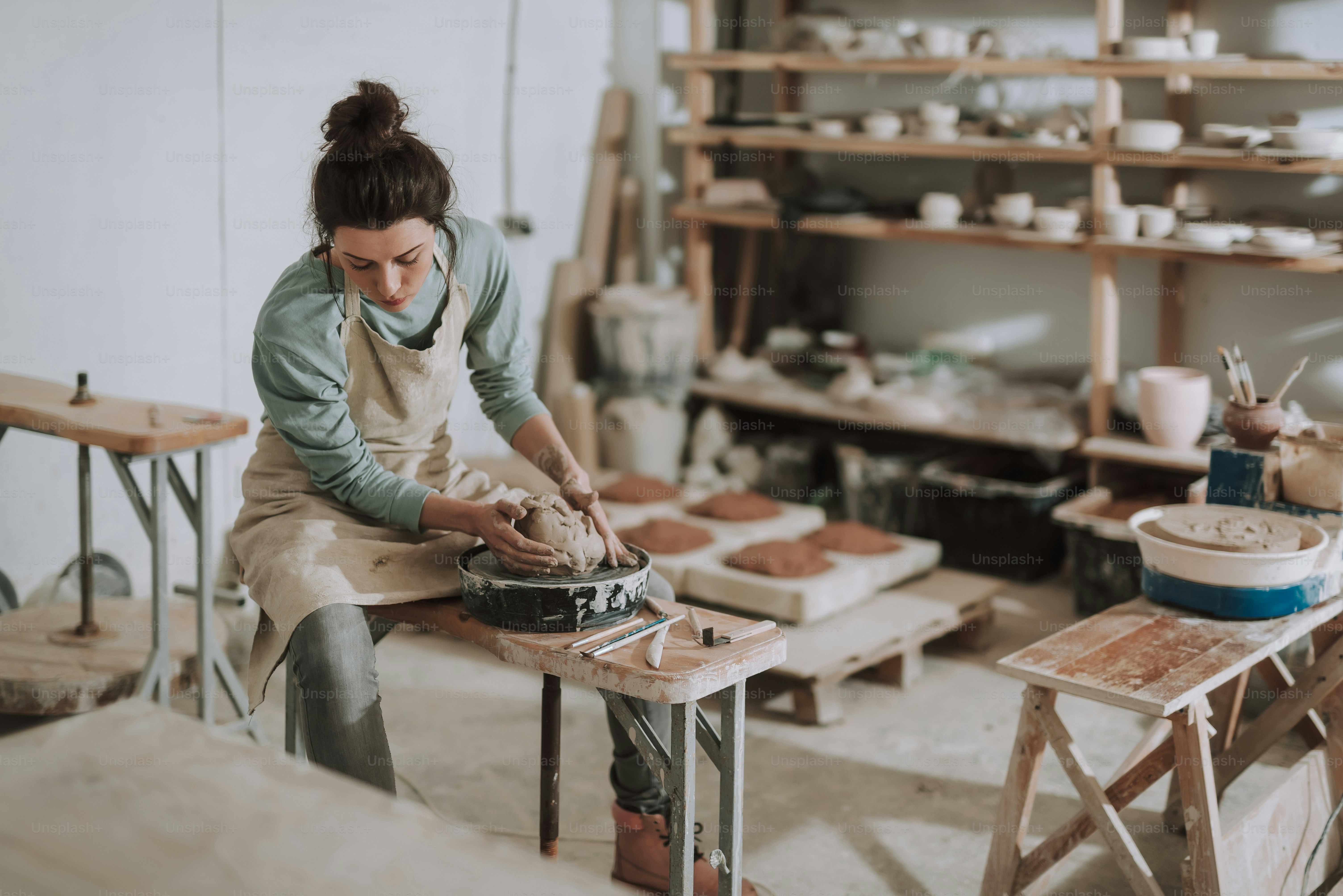 Portrait of charming craftswoman sitting on bench while kneading and ...