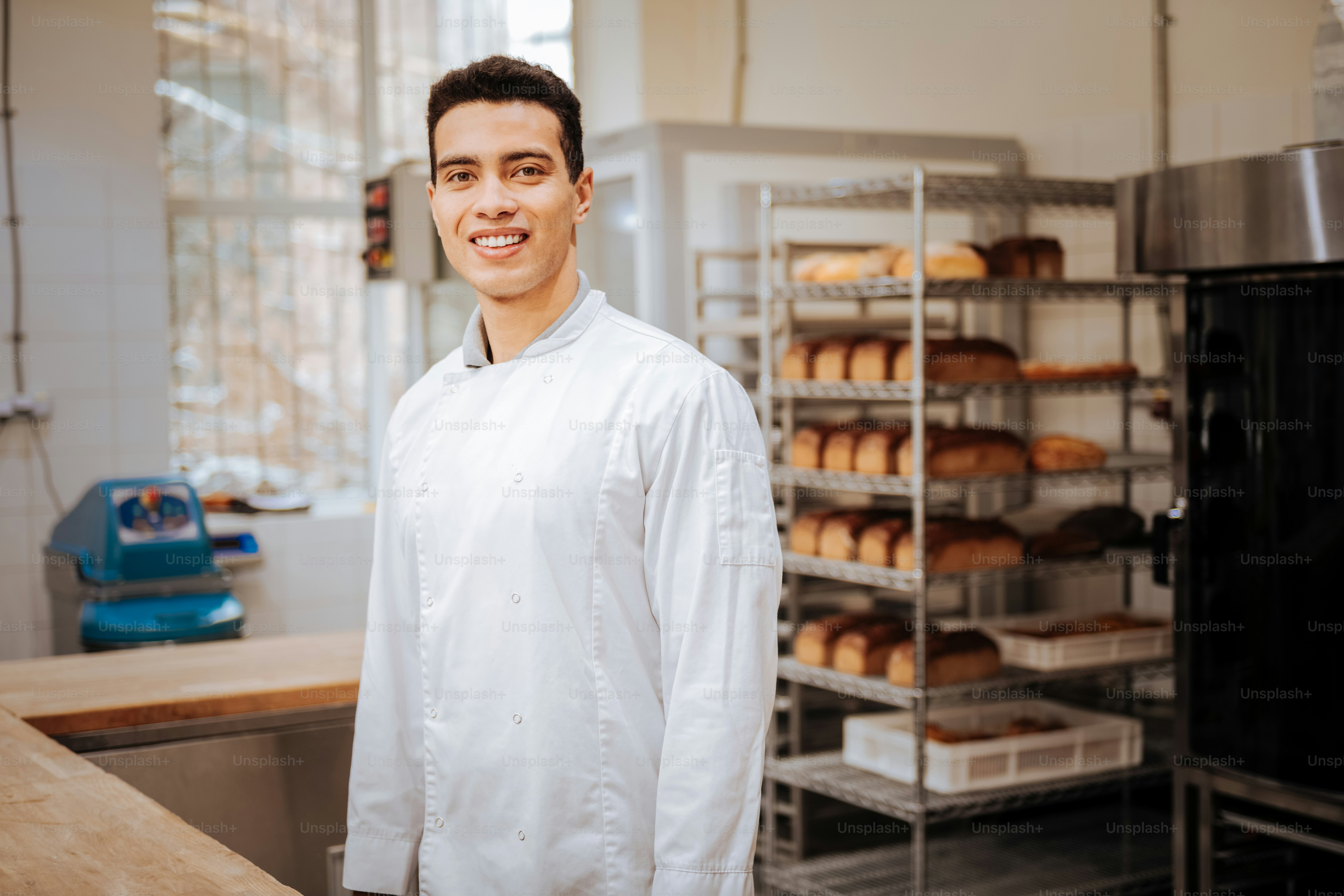 Baker smiling. Young dark-haired professional baker smiling while ...