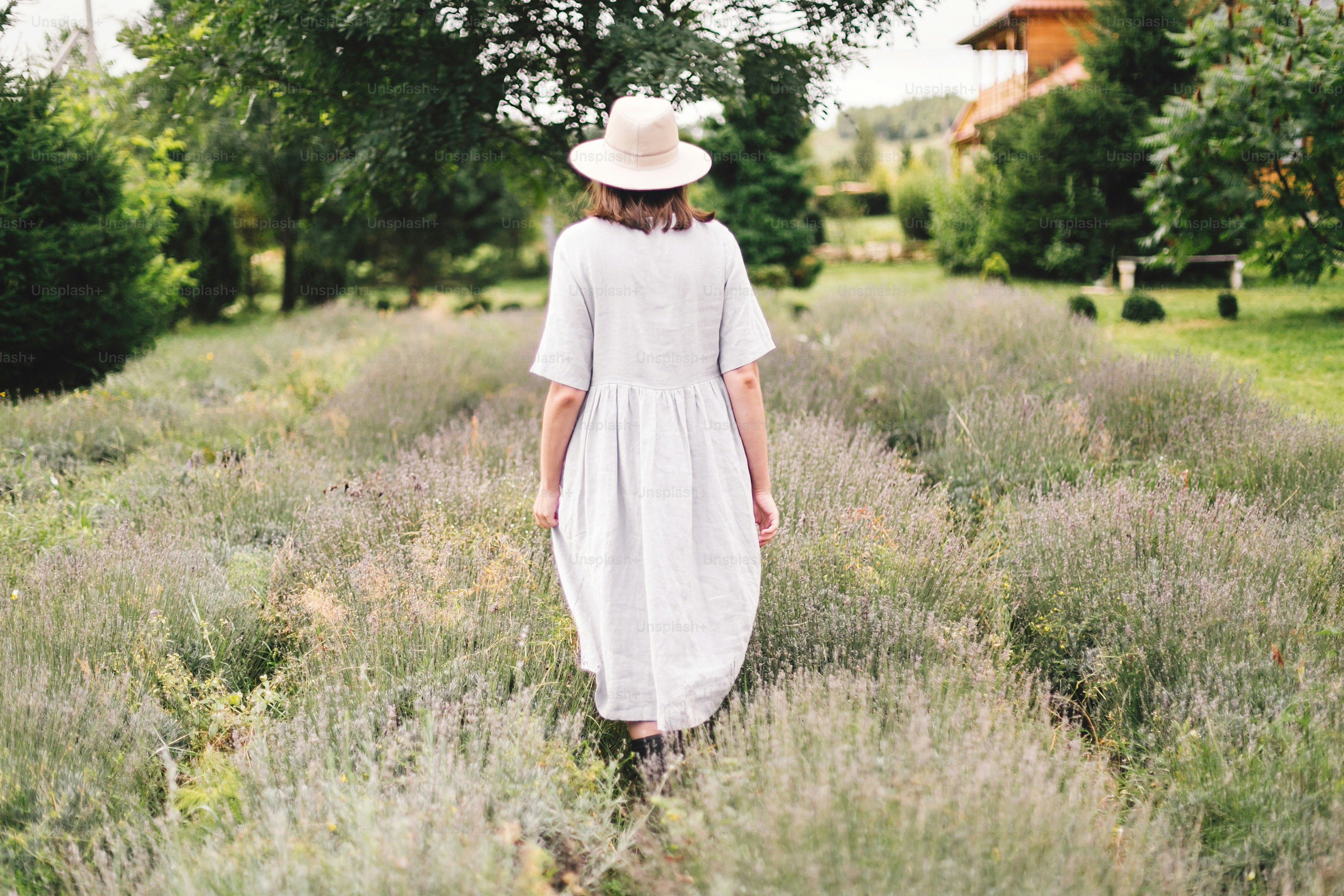 Stylish hipster girl in linen dress and hat walking in lavender field ...