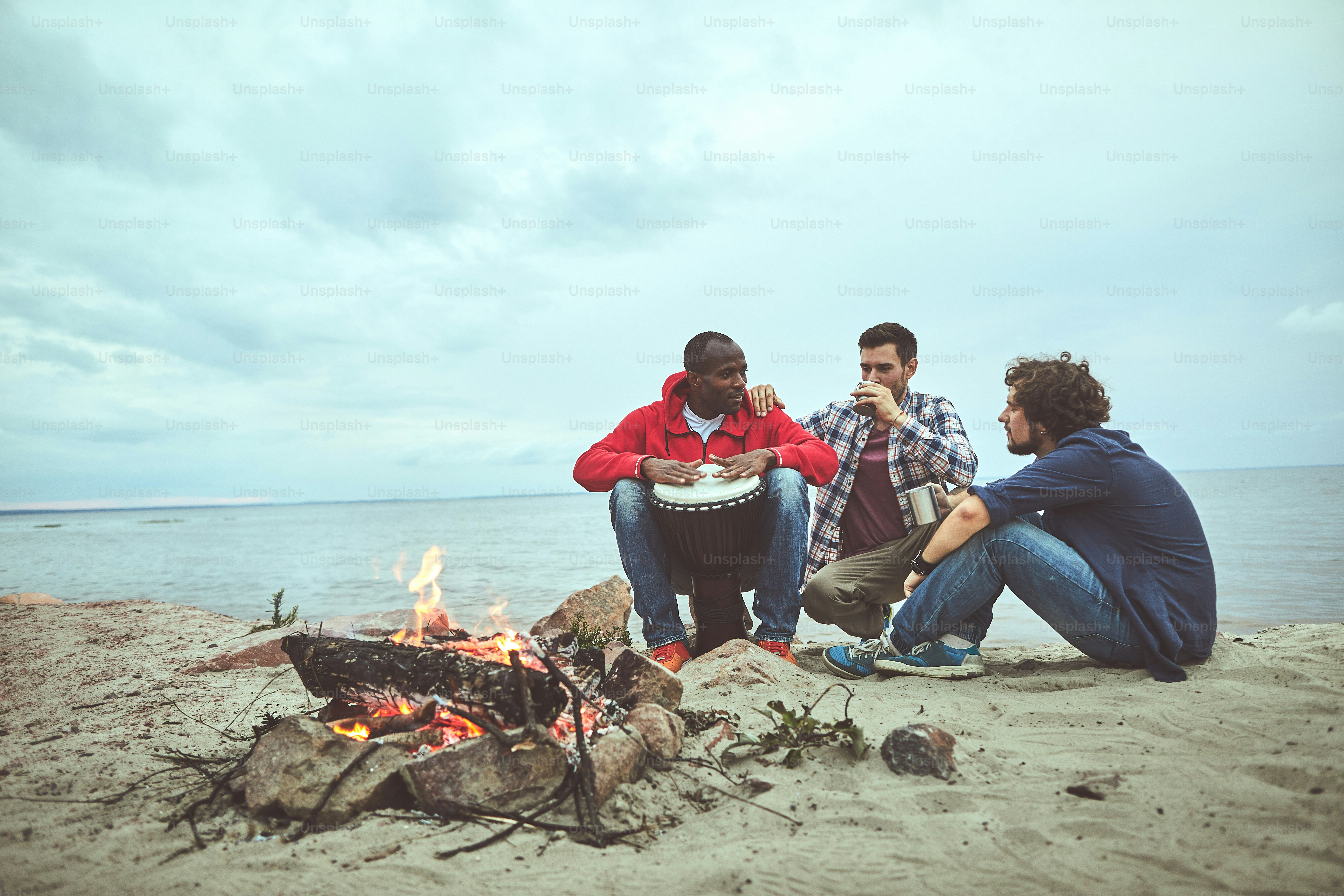 Folk theme. Three young friends spending time at the bonfire while one ...