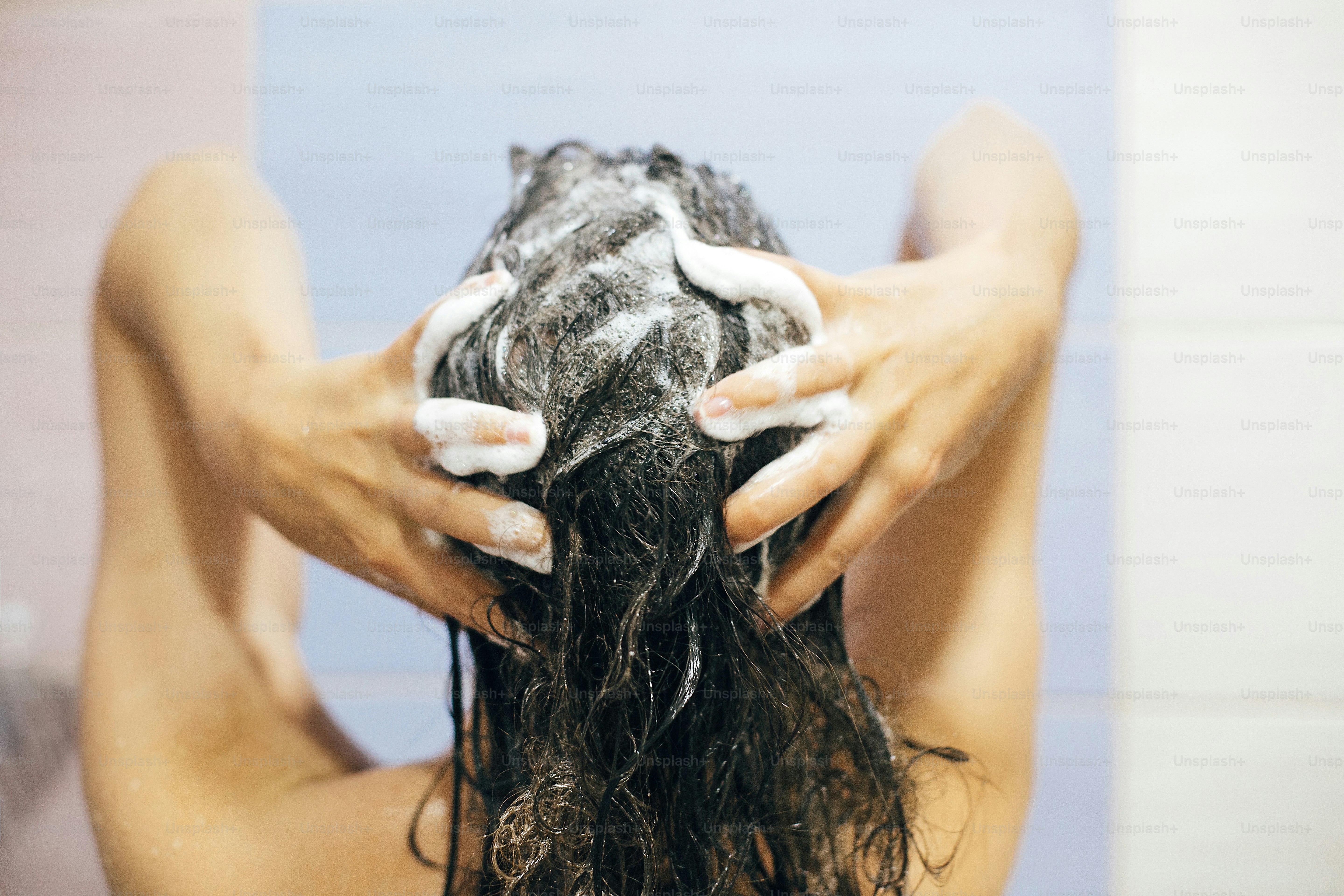 Young happy woman washing her hair with shampoo, hands with foam ...
