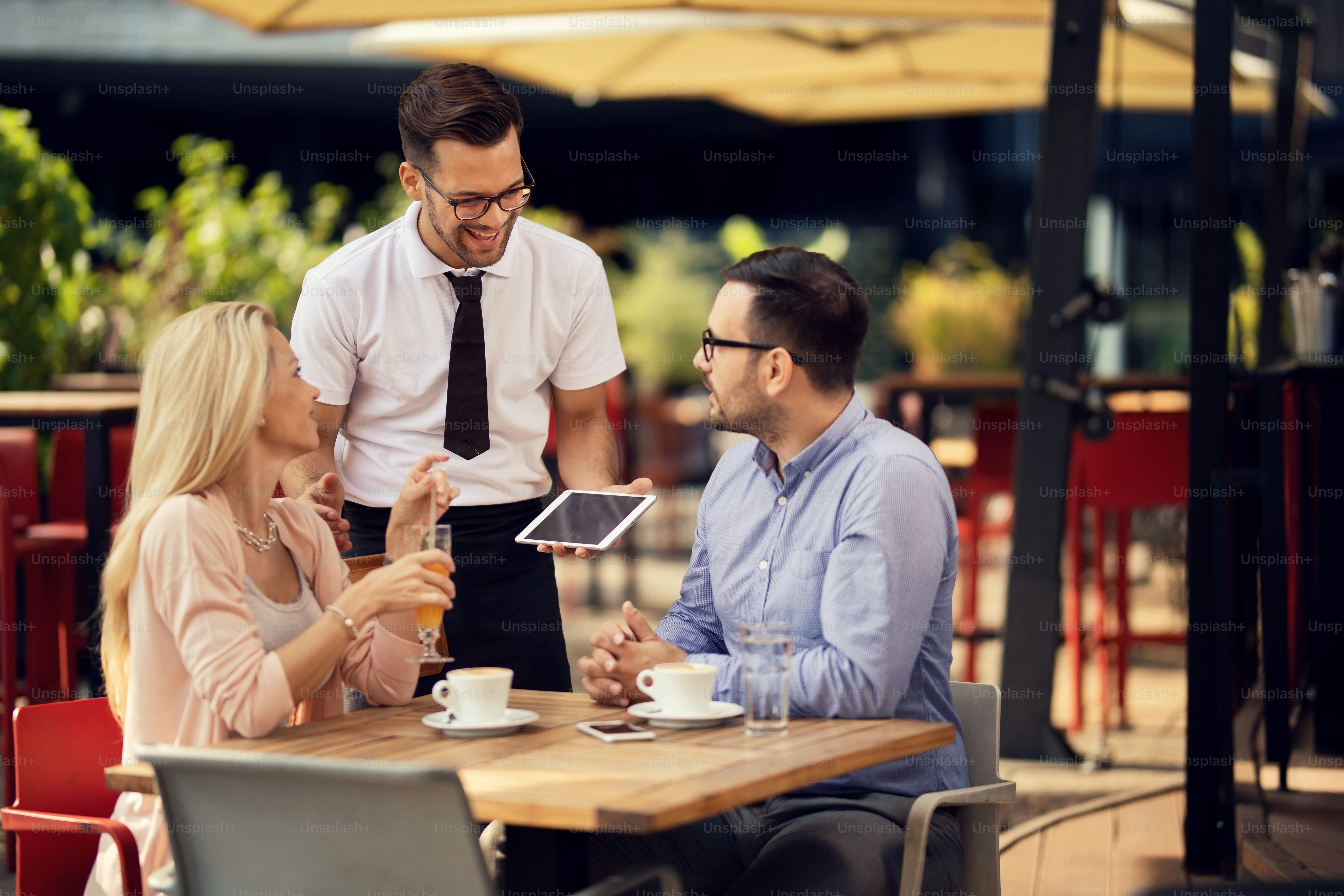 Young happy waiter communicating with guests in an outdoor cafe. photo ...