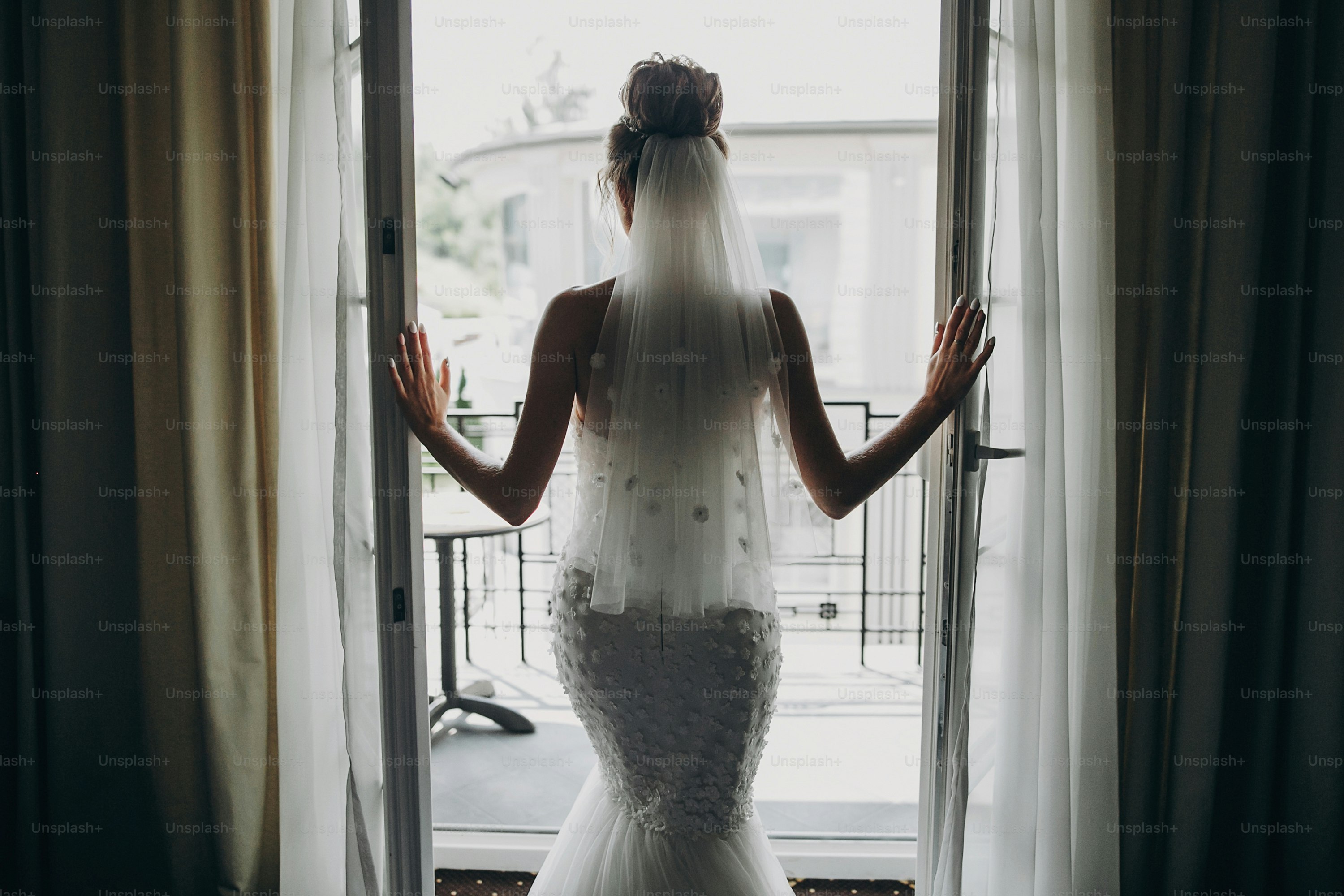 Silhouette of stylish bride opening window balcony in soft light in ...