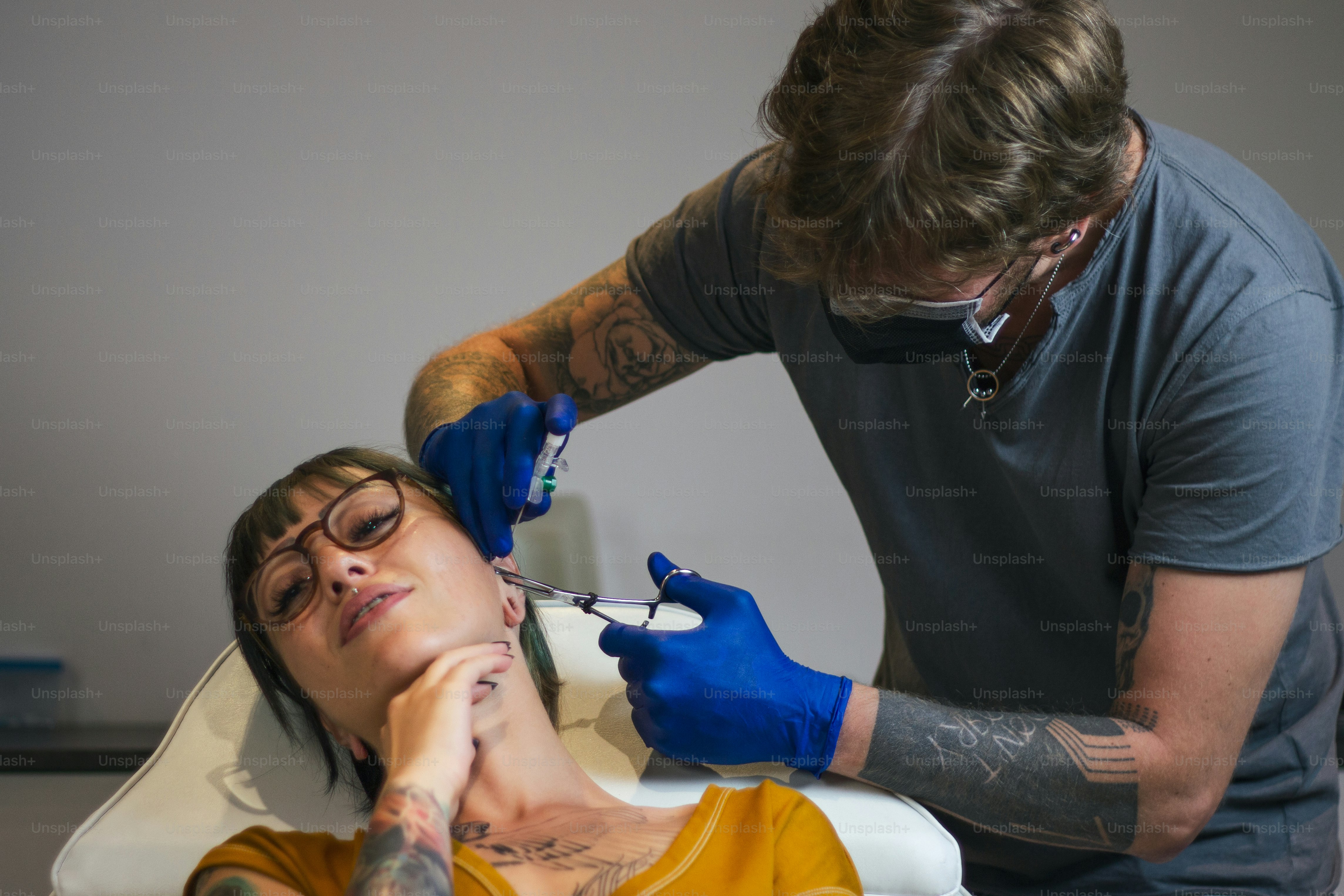 Mujer joven haciéndose un piercing en la oreja. Hombre mostrando un ...
