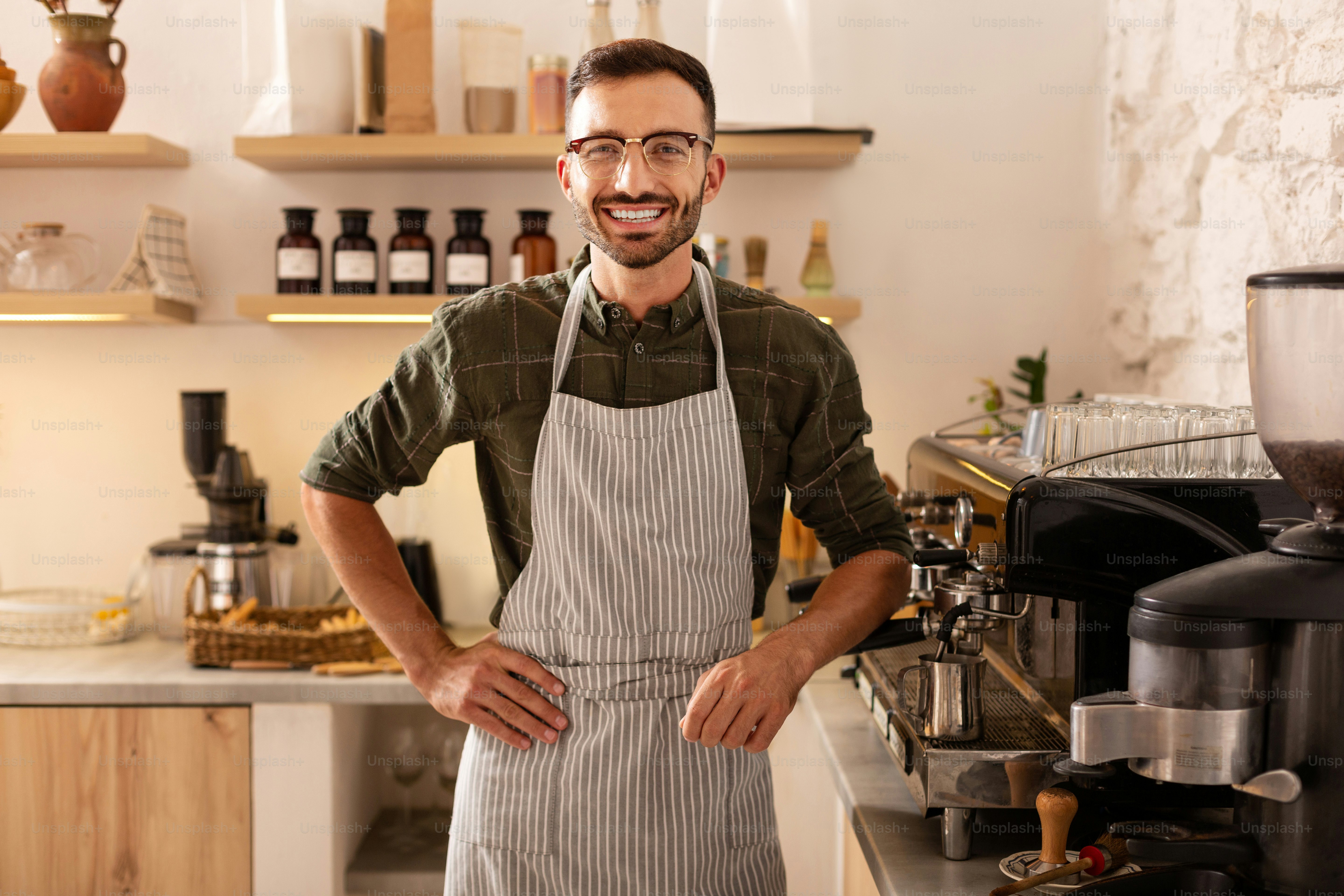 Cheerful barista. Cheerful dark-haired bearded barista smiling while ...