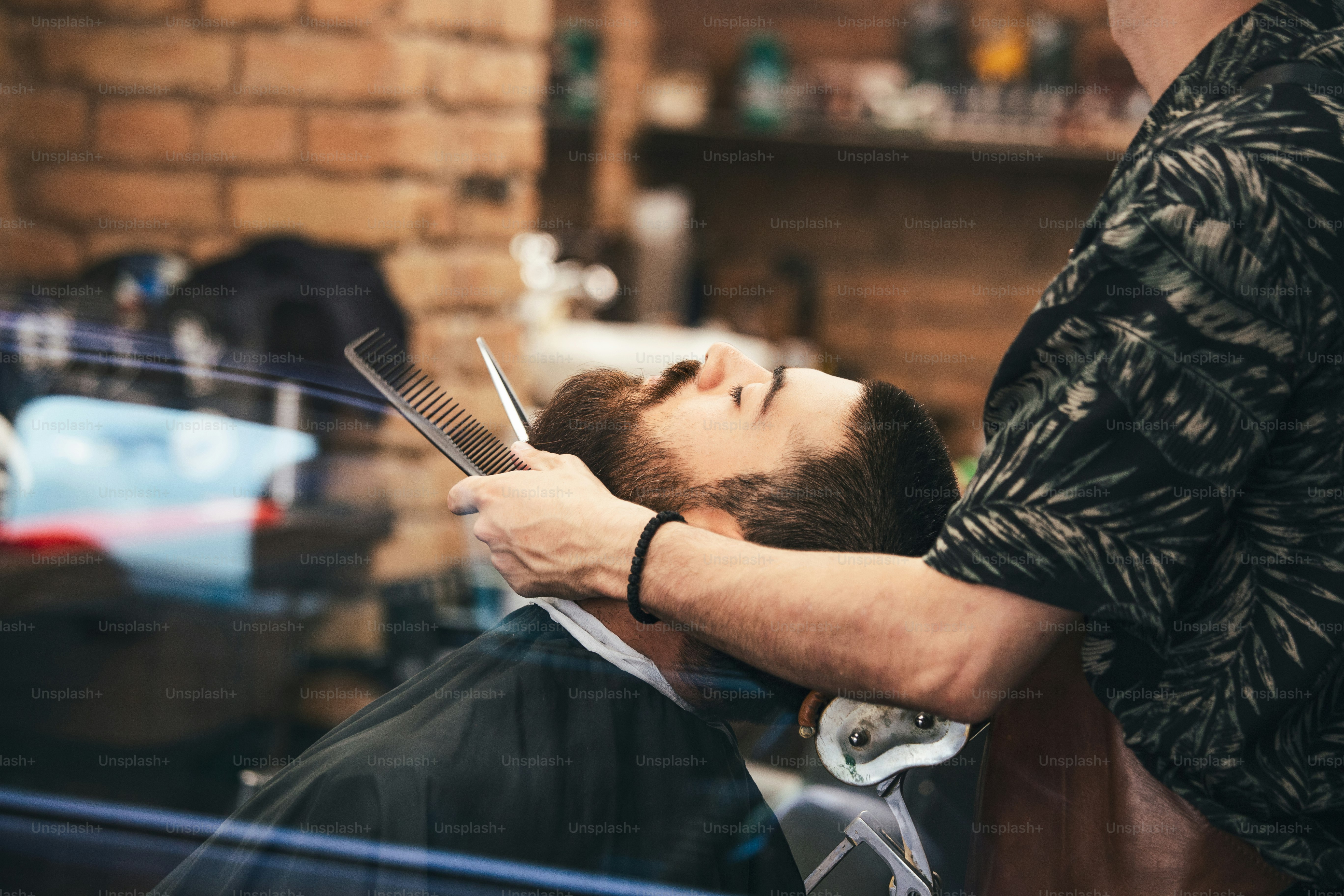 Bearded male sitting in an armchair in a barber shop while hairdresser ...