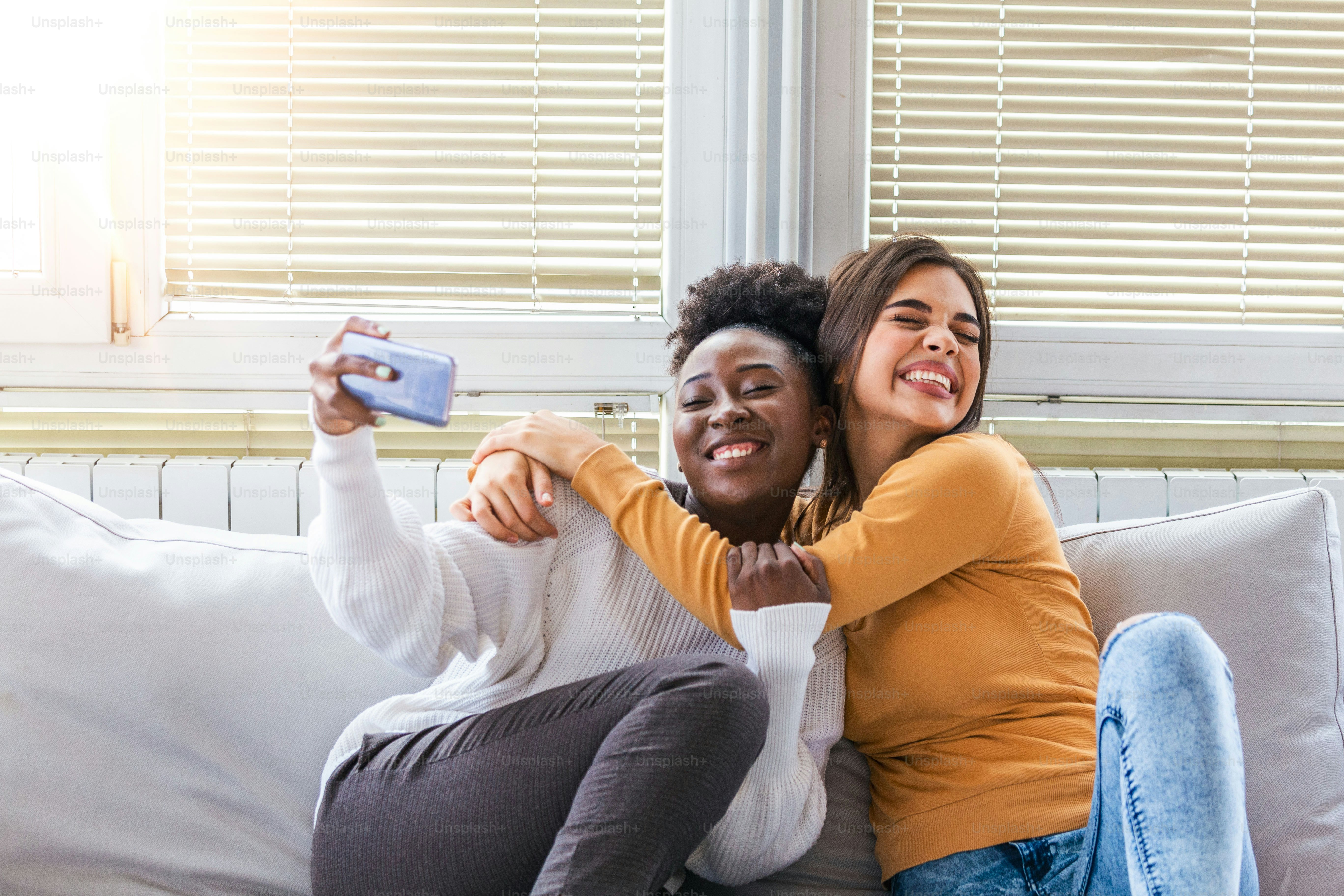 Des amies qui rient s’étreignent sur le canapé tout en prenant une ...