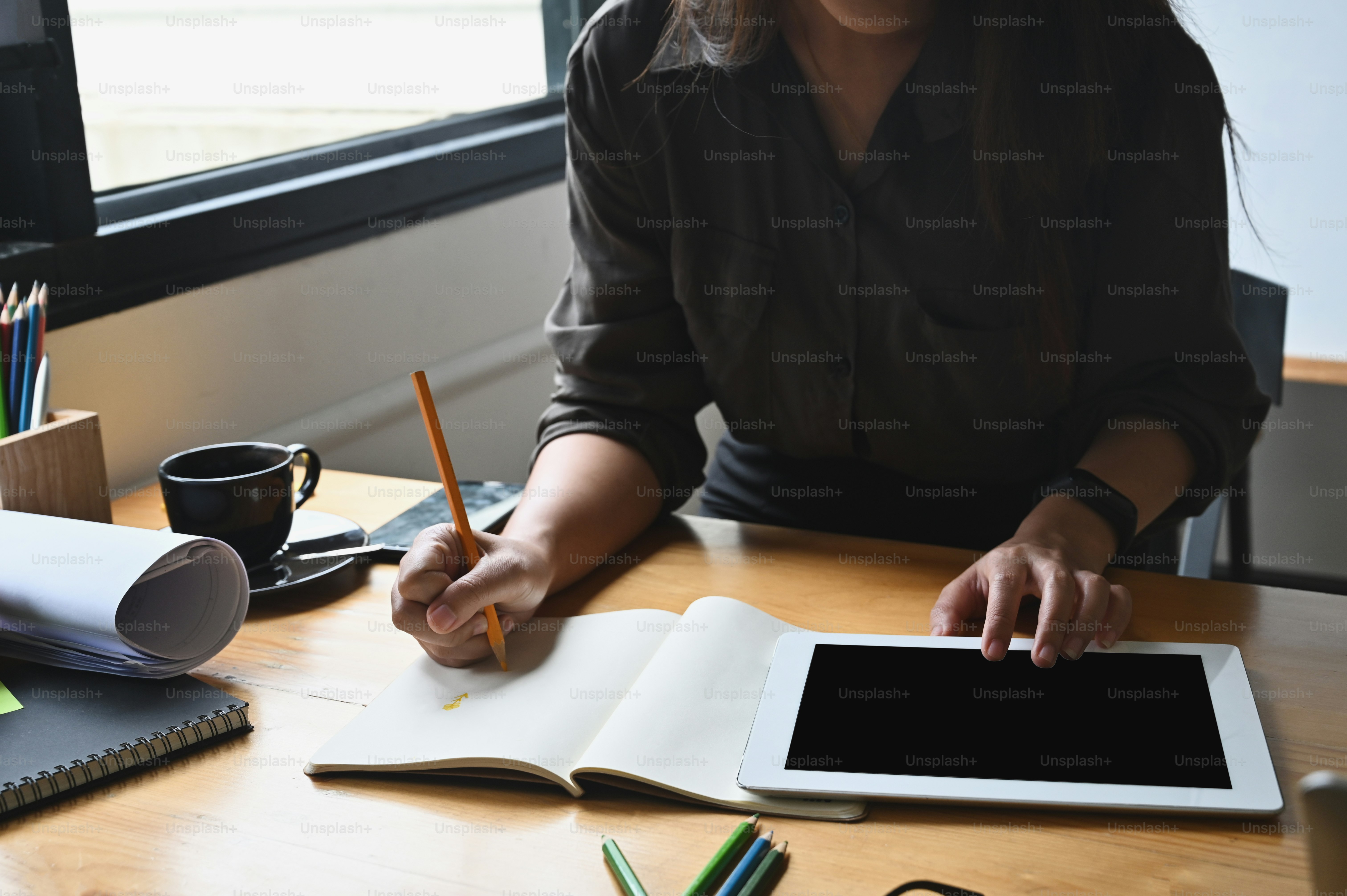 Young creative woman writing on notebook and using tablet computer ...