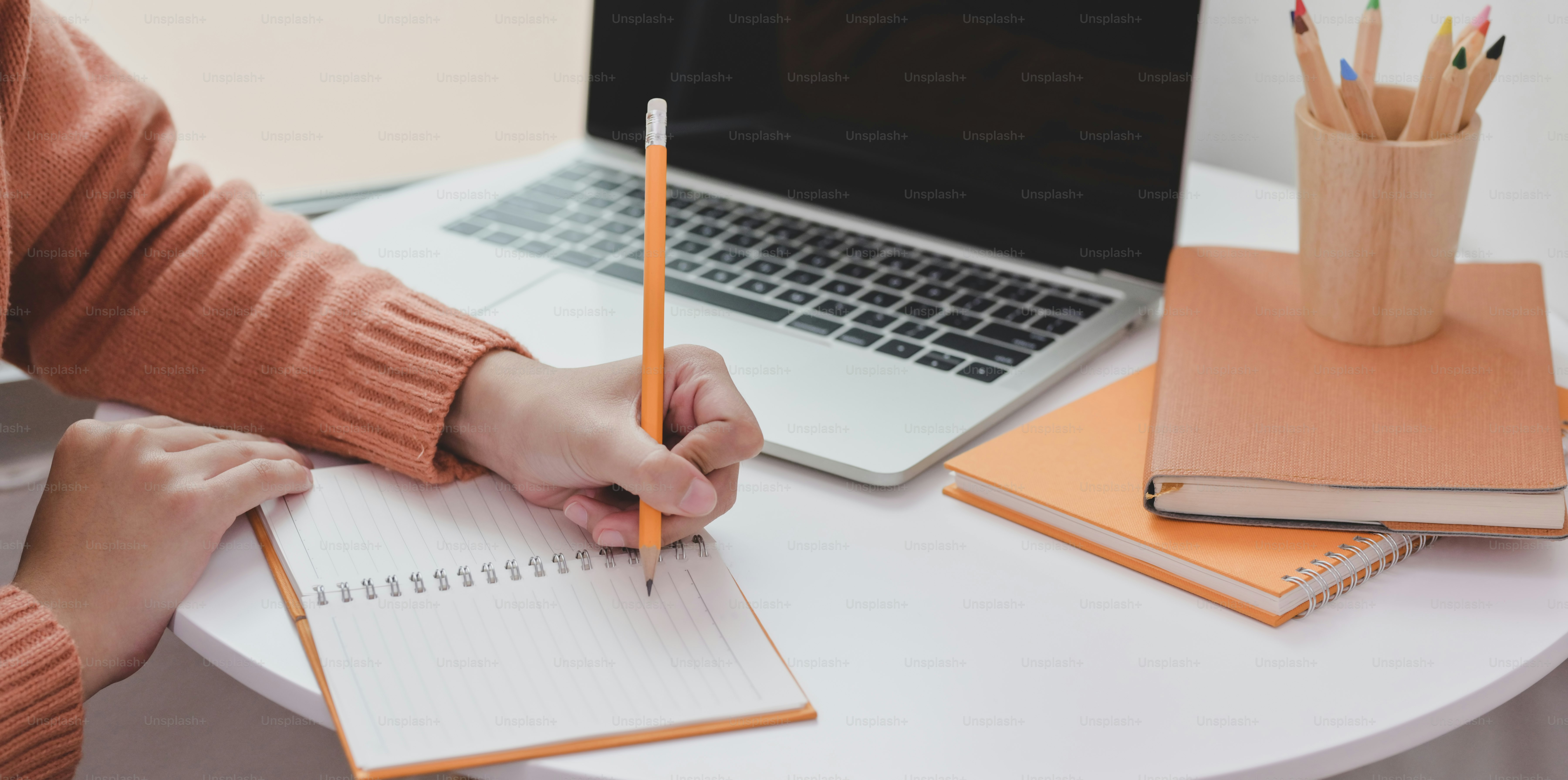 Close-up view of young woman working on her project while drafting her idea on notebook in ...