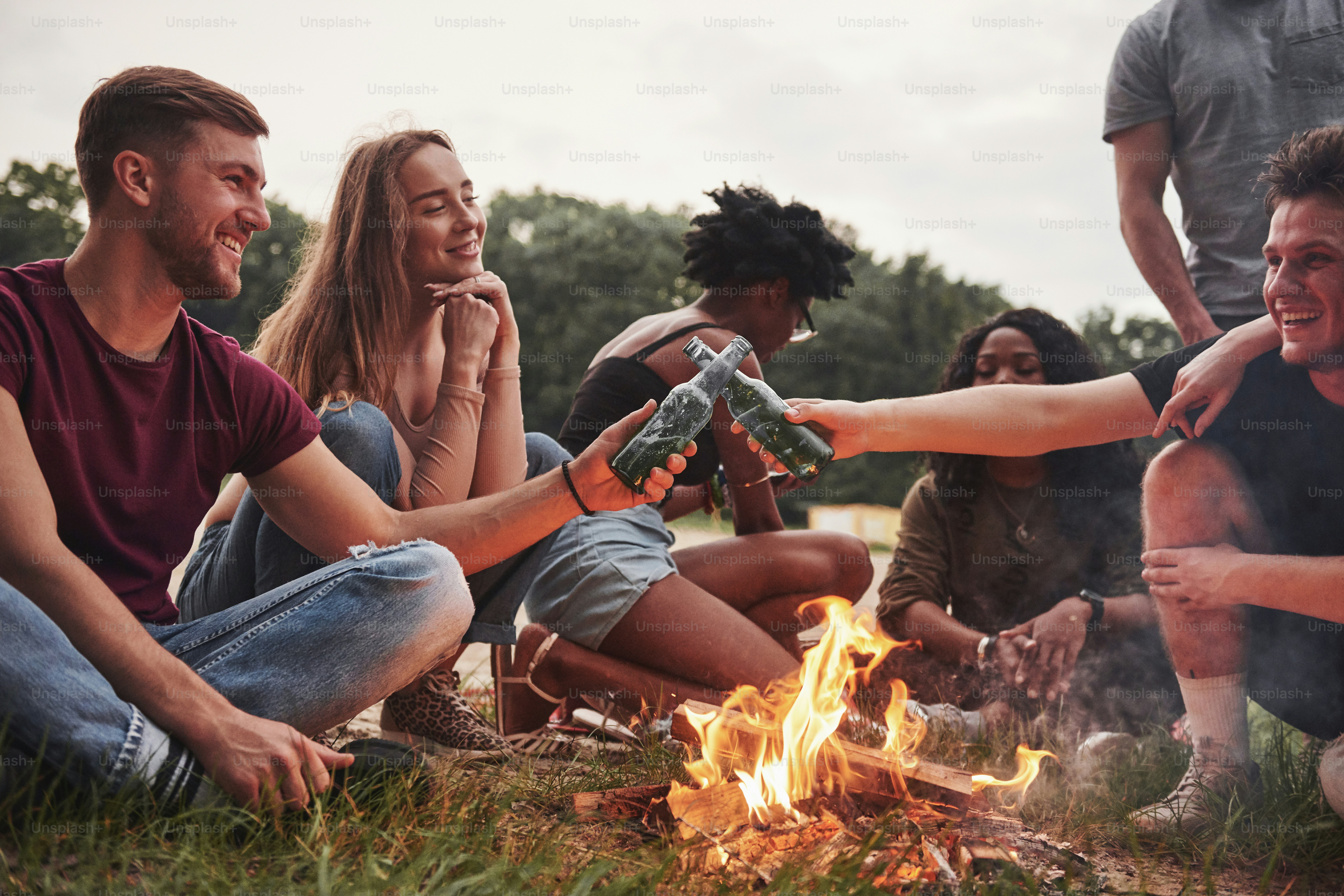 Bottles crossed. Group of people have picnic on the beach. Friends have ...