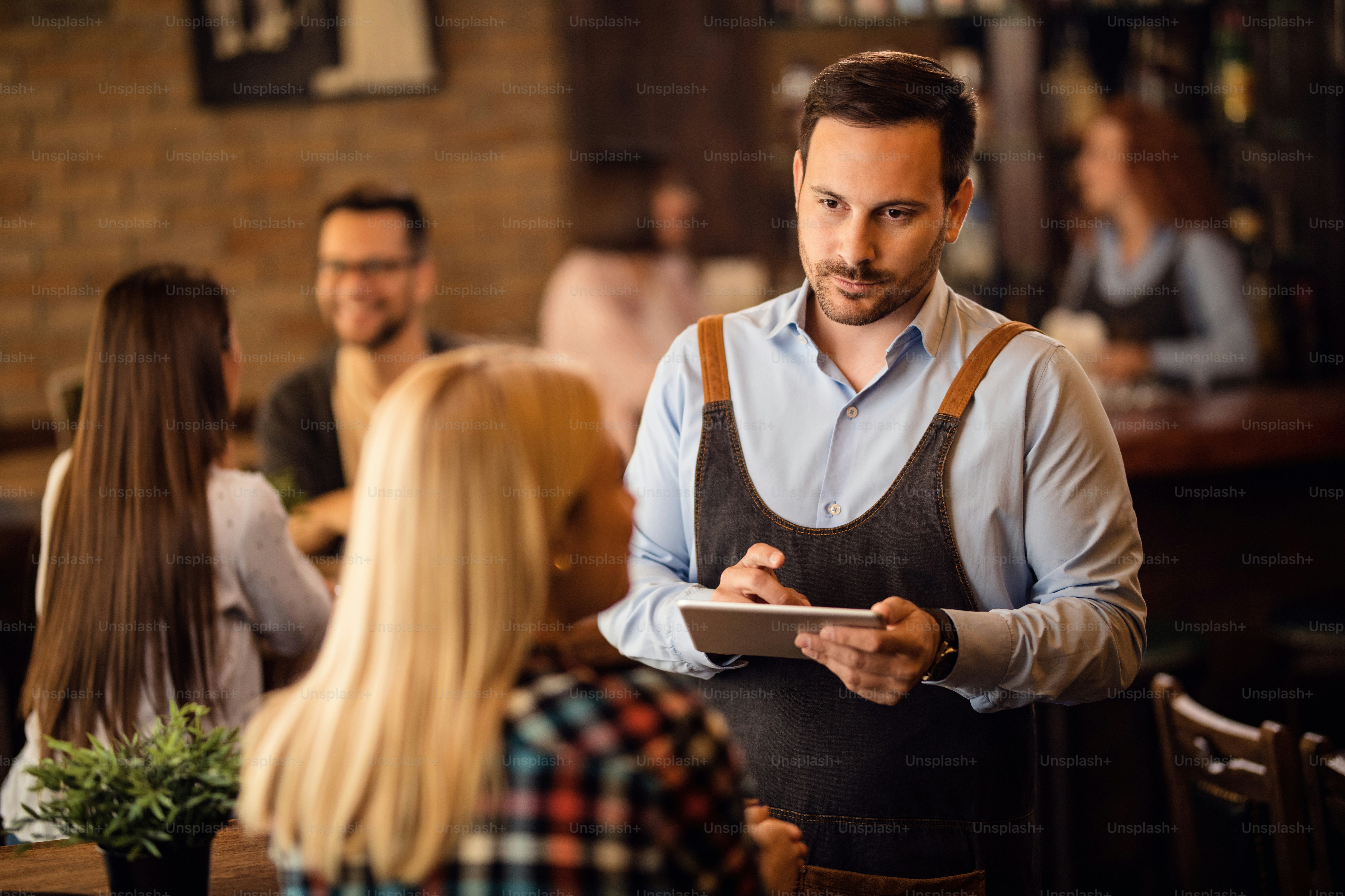 Mid adult waiter using digital tablet and writing an order while ...