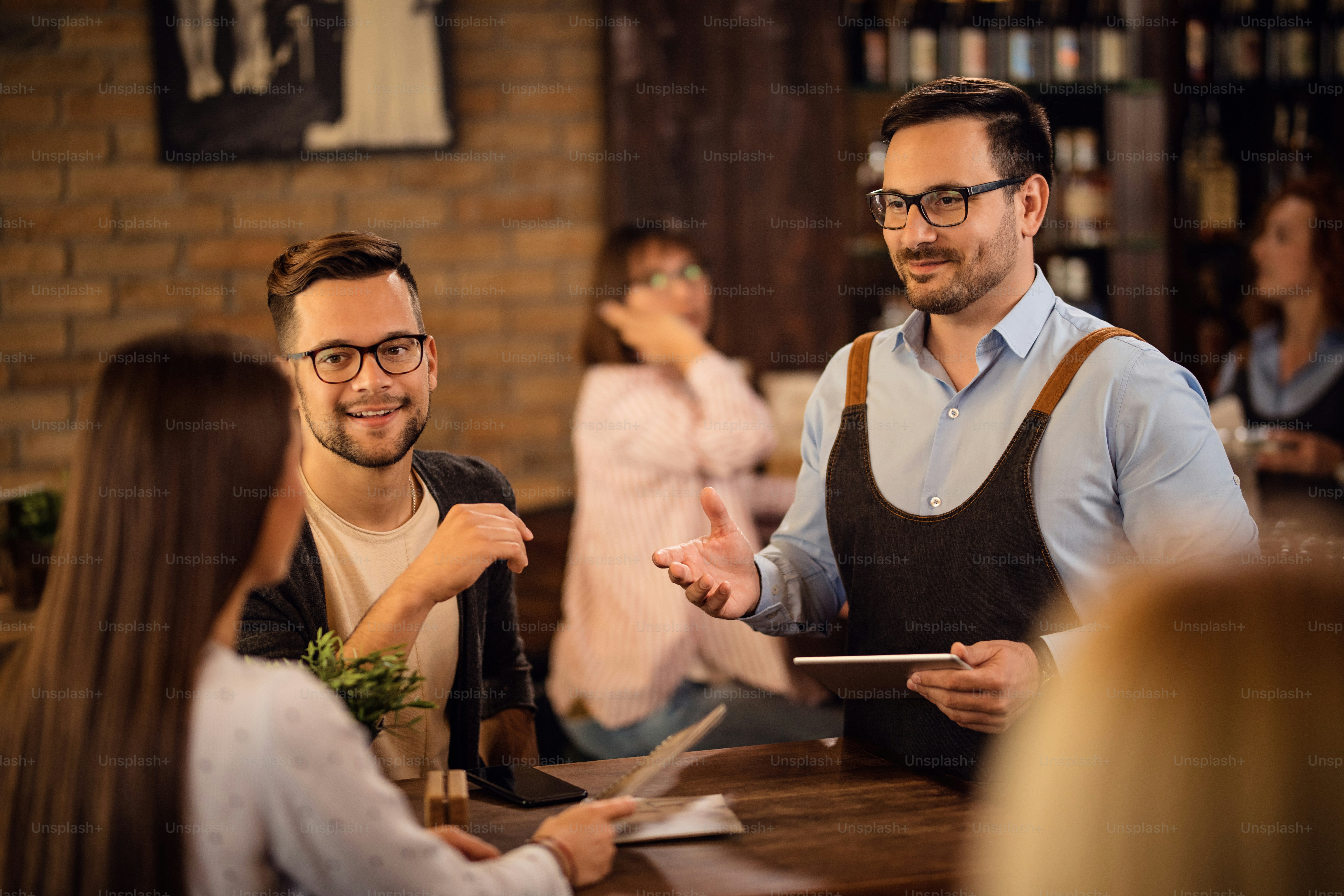 Smiling waiter with digital tablet taking order while talking with a ...