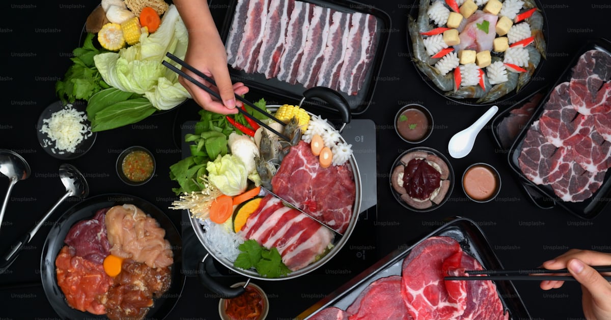 신선한 얇게 썬 고기 바다 음식 검은 배경의 야채 일본 요리와 함께 냄비에서 샤브샤브를 먹는 사람들의 상위 뷰 사진