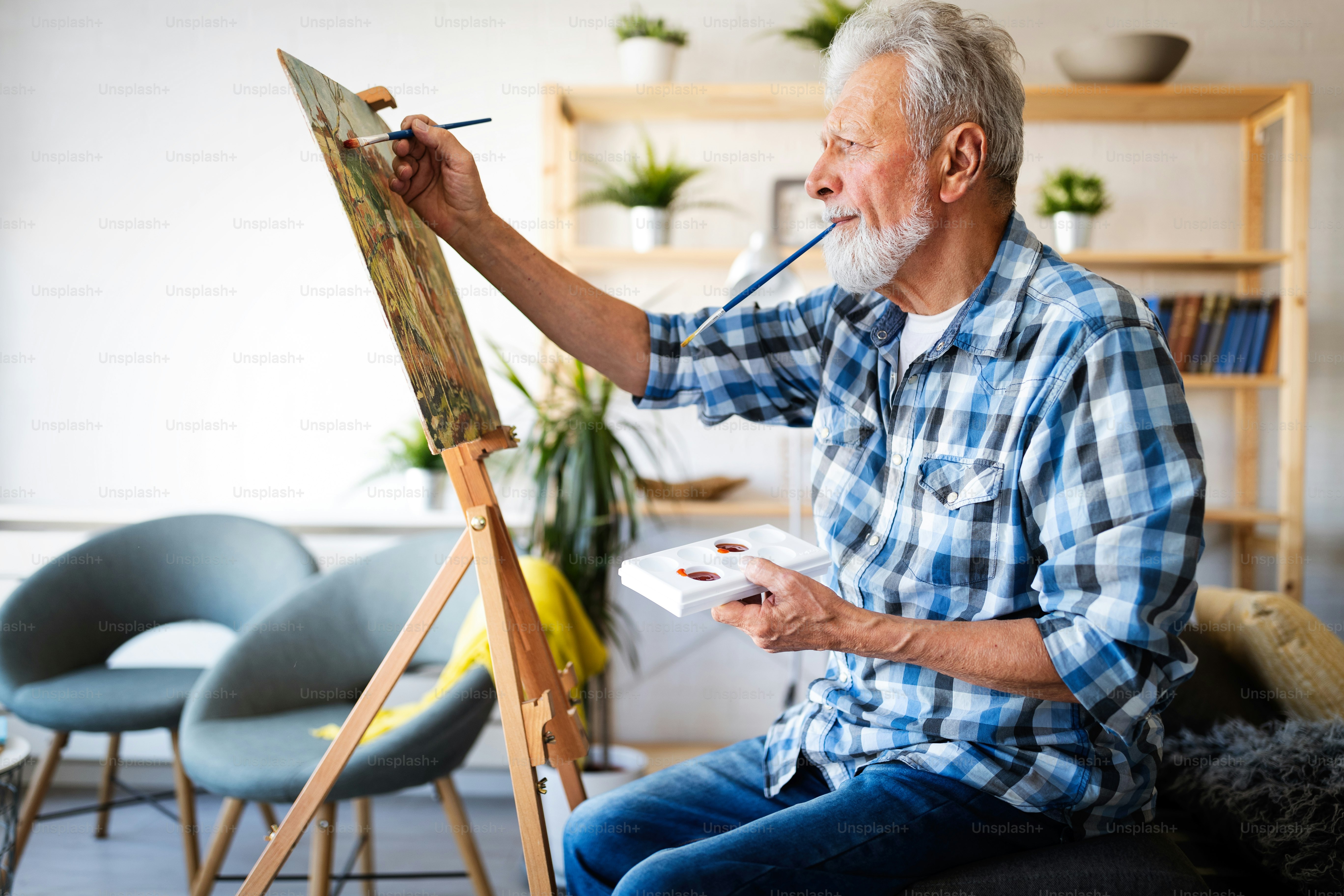 Handsome senior man artist paints on canvas painting on the easel photo ...