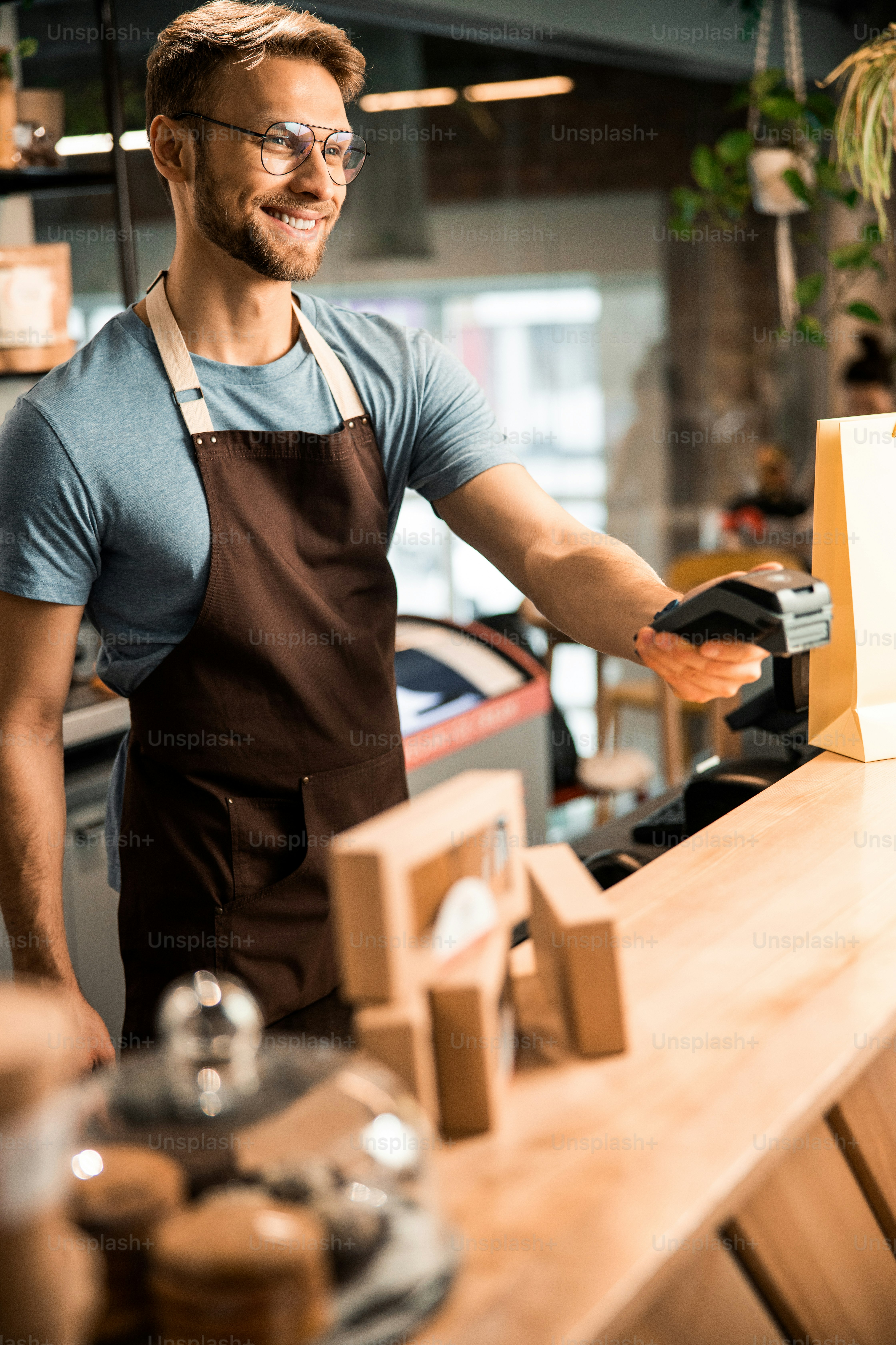 Smiling man standing behind the counter at the coffee shop and giving ...